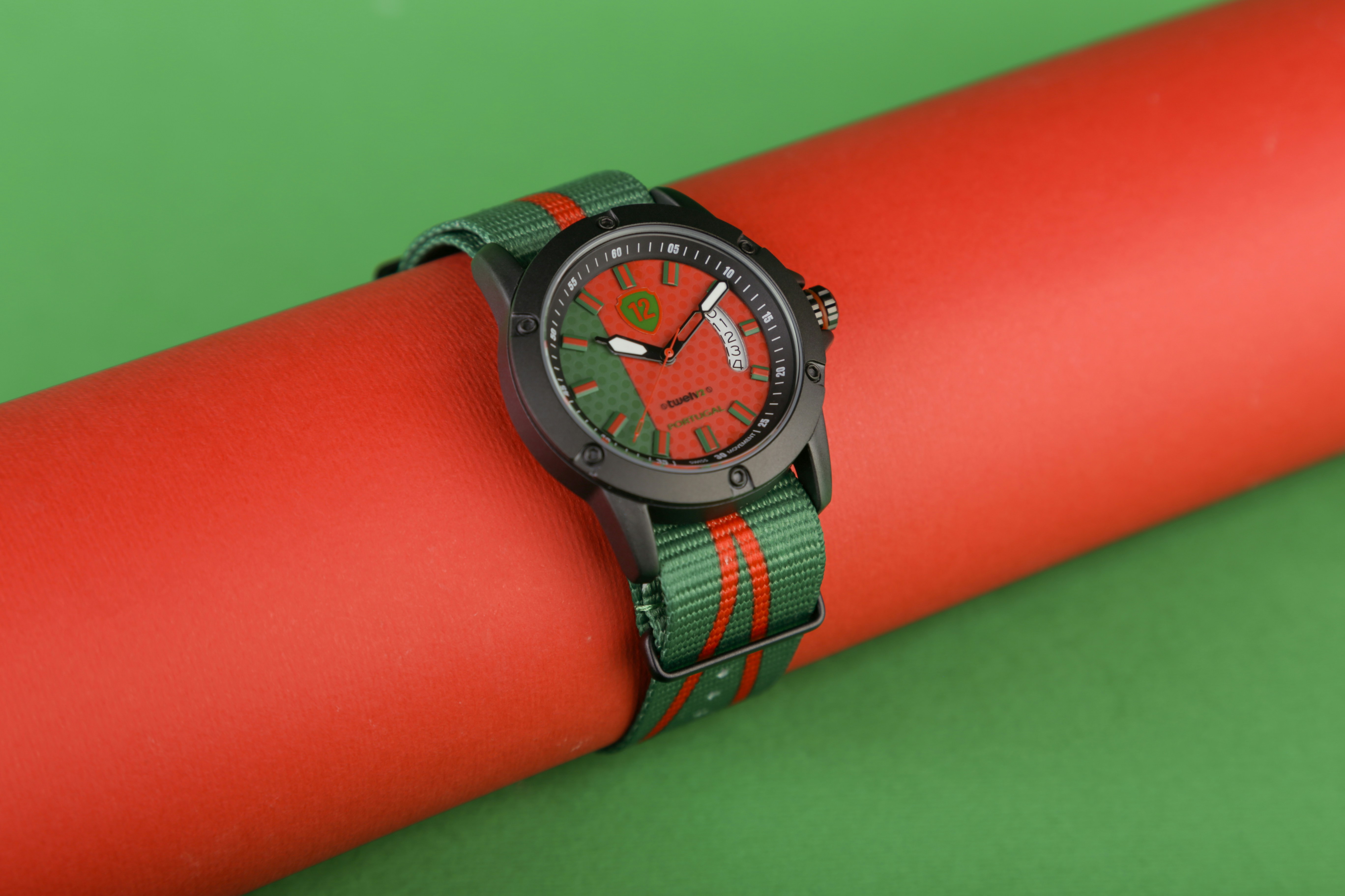 Color-Blocking Timepiece: A Green-Red Strap Watch Resting on a Bold Cylinder