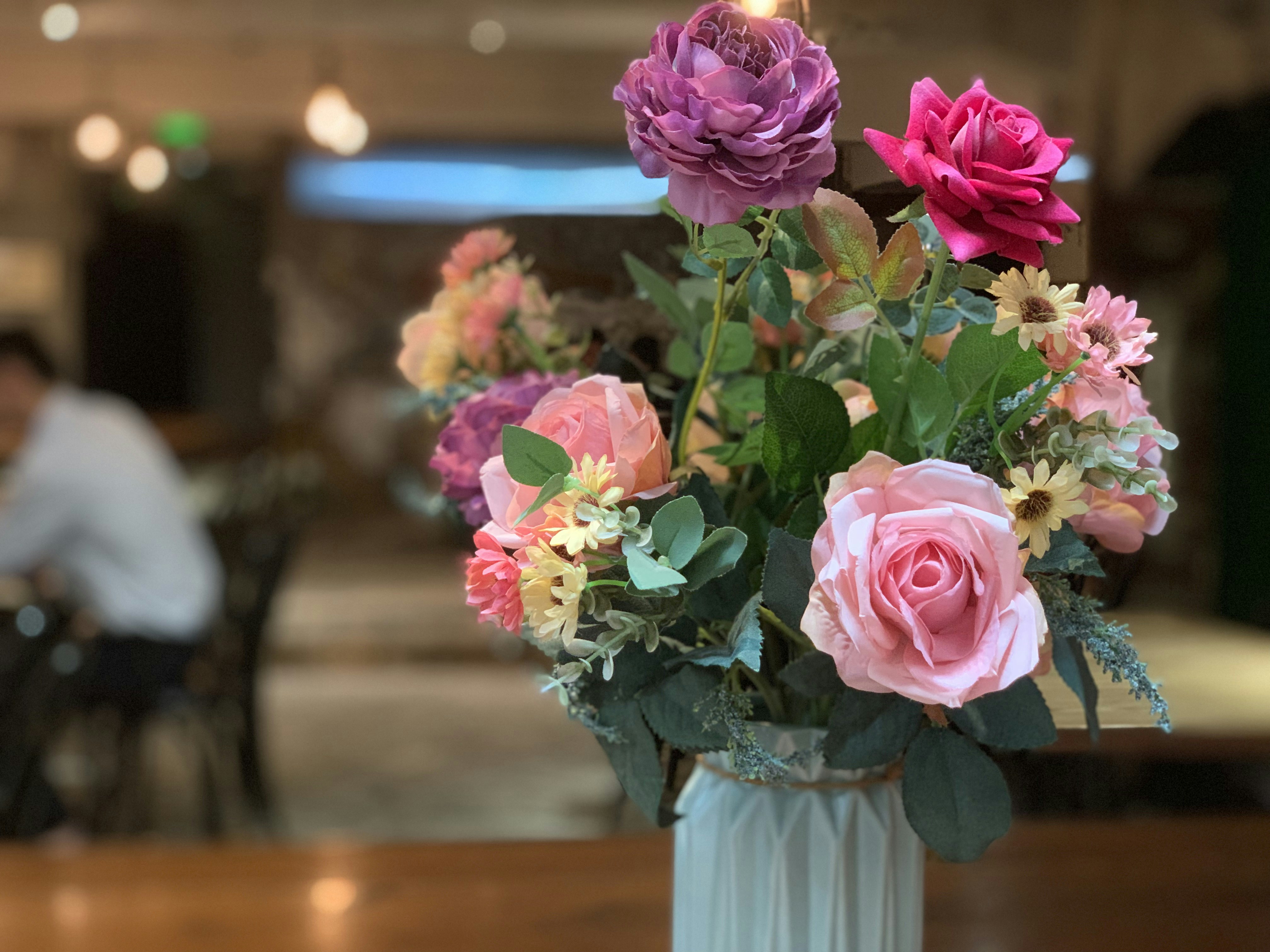 Vibrant bouquet featuring pink and purple flowers in a decorative vase, set against a softly blurred background. 