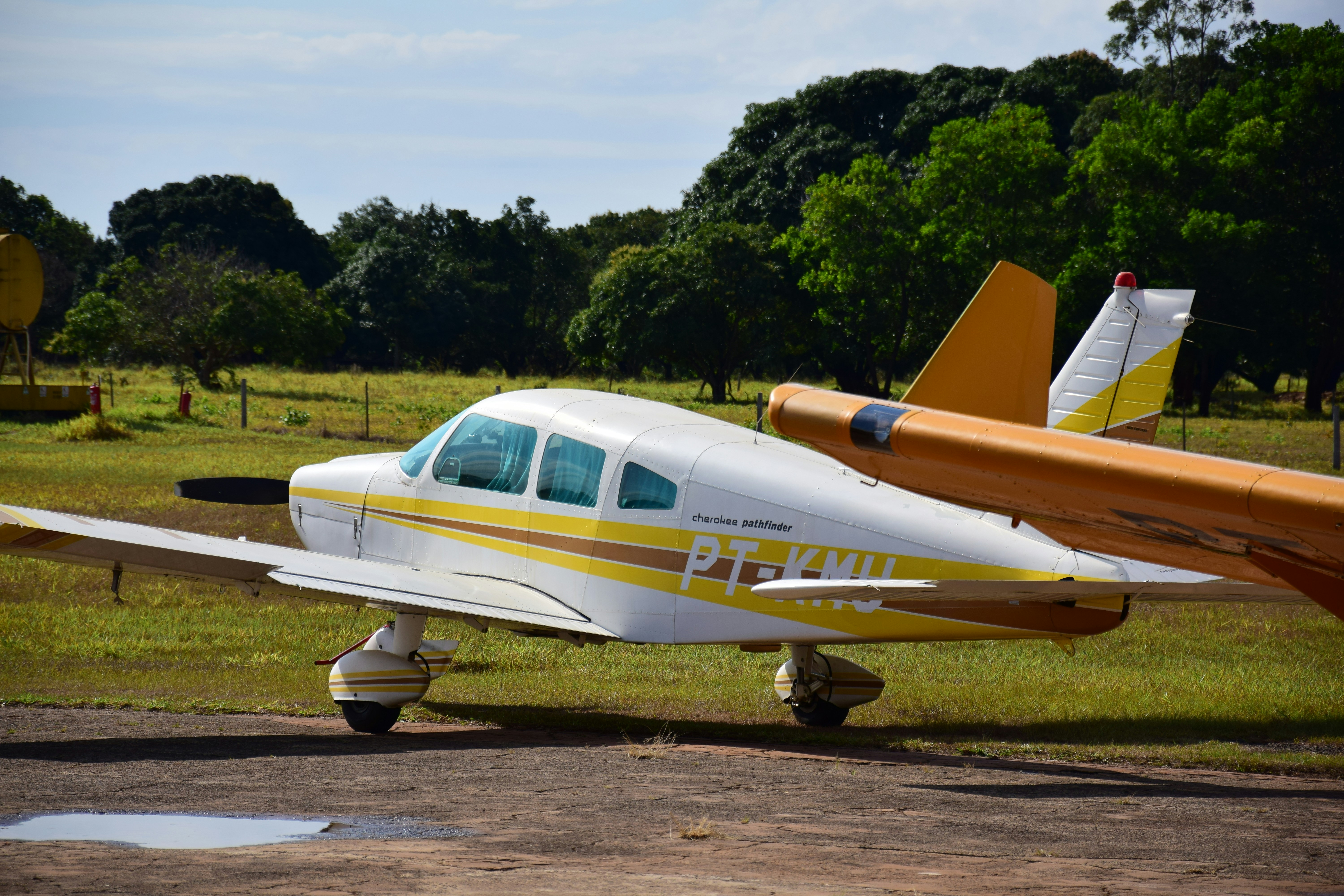 Gold-Striped Light Aircraft Resting on a Sunlit Grass Runway