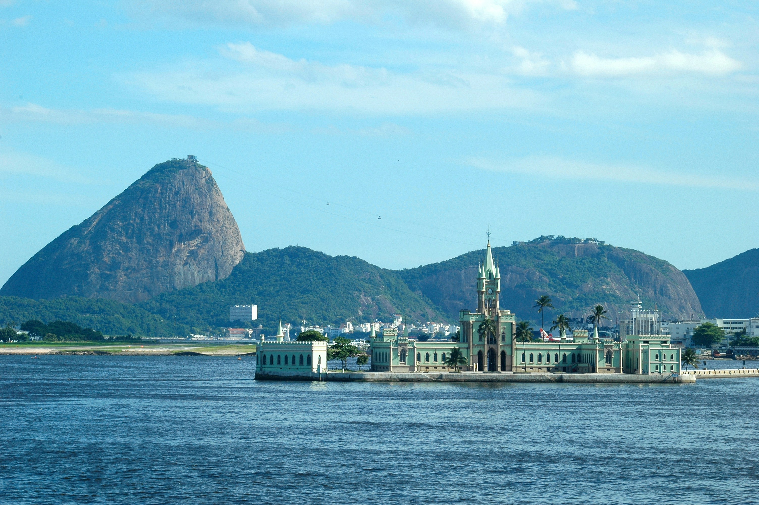 Historic building on an island surrounded by water, with a mountainous backdrop under a clear blue sky.