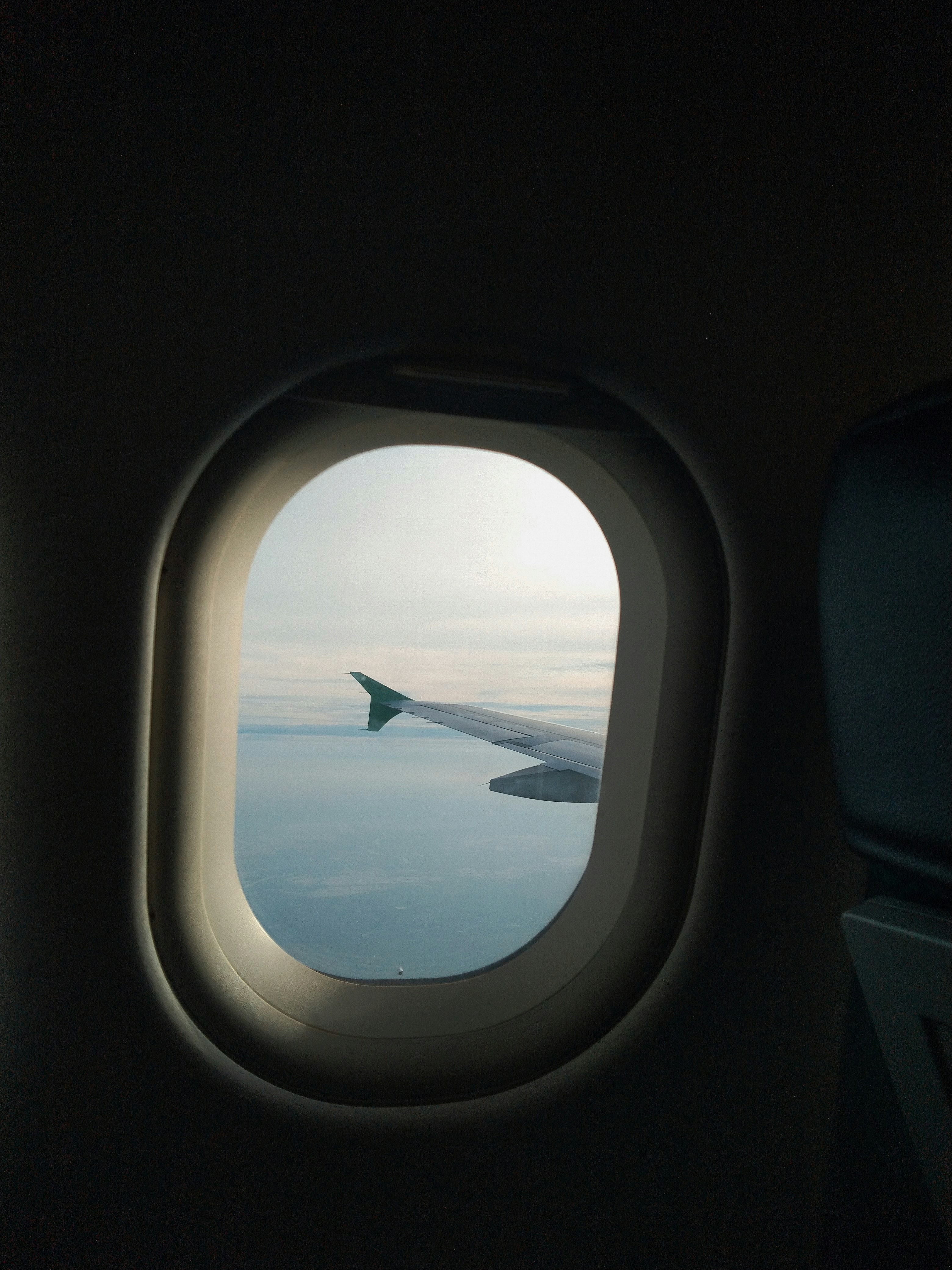 Airplane wing framed by a window against a vast sky.