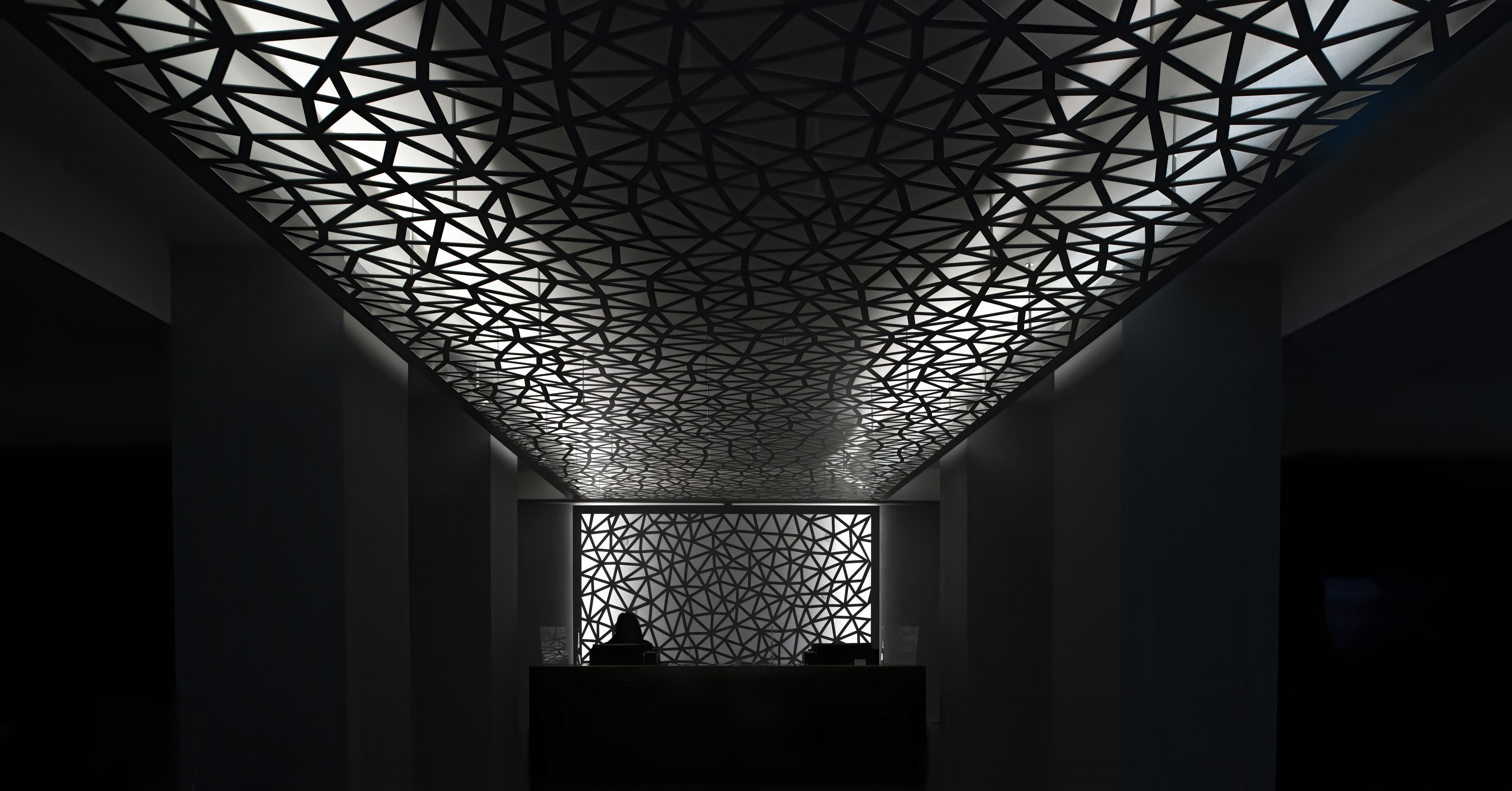 Intricate geometric ceiling design illuminated by soft lighting in a contemporary reception area.