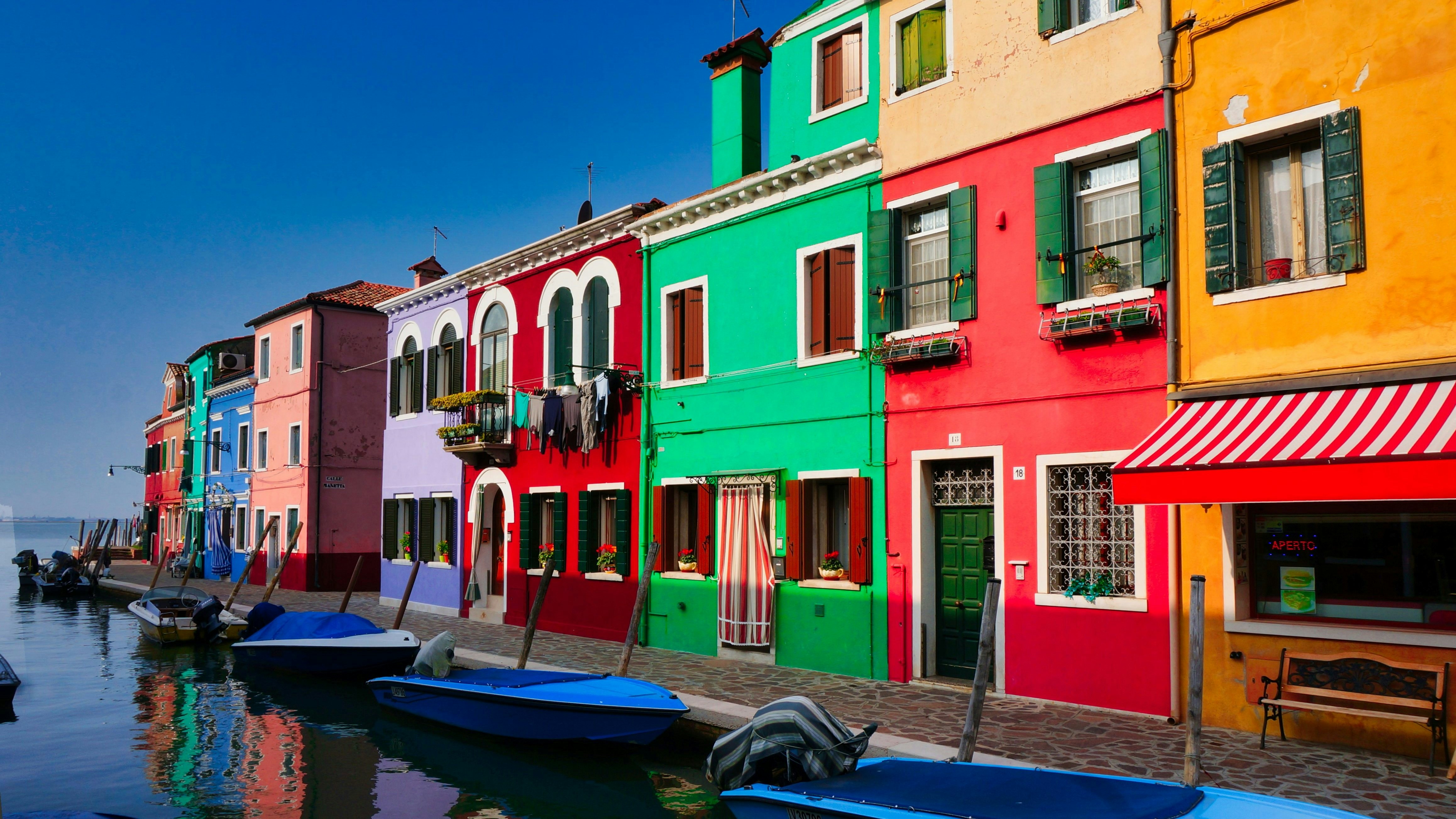 Colorful houses line a canal with boats moored alongside under a clear blue sky.