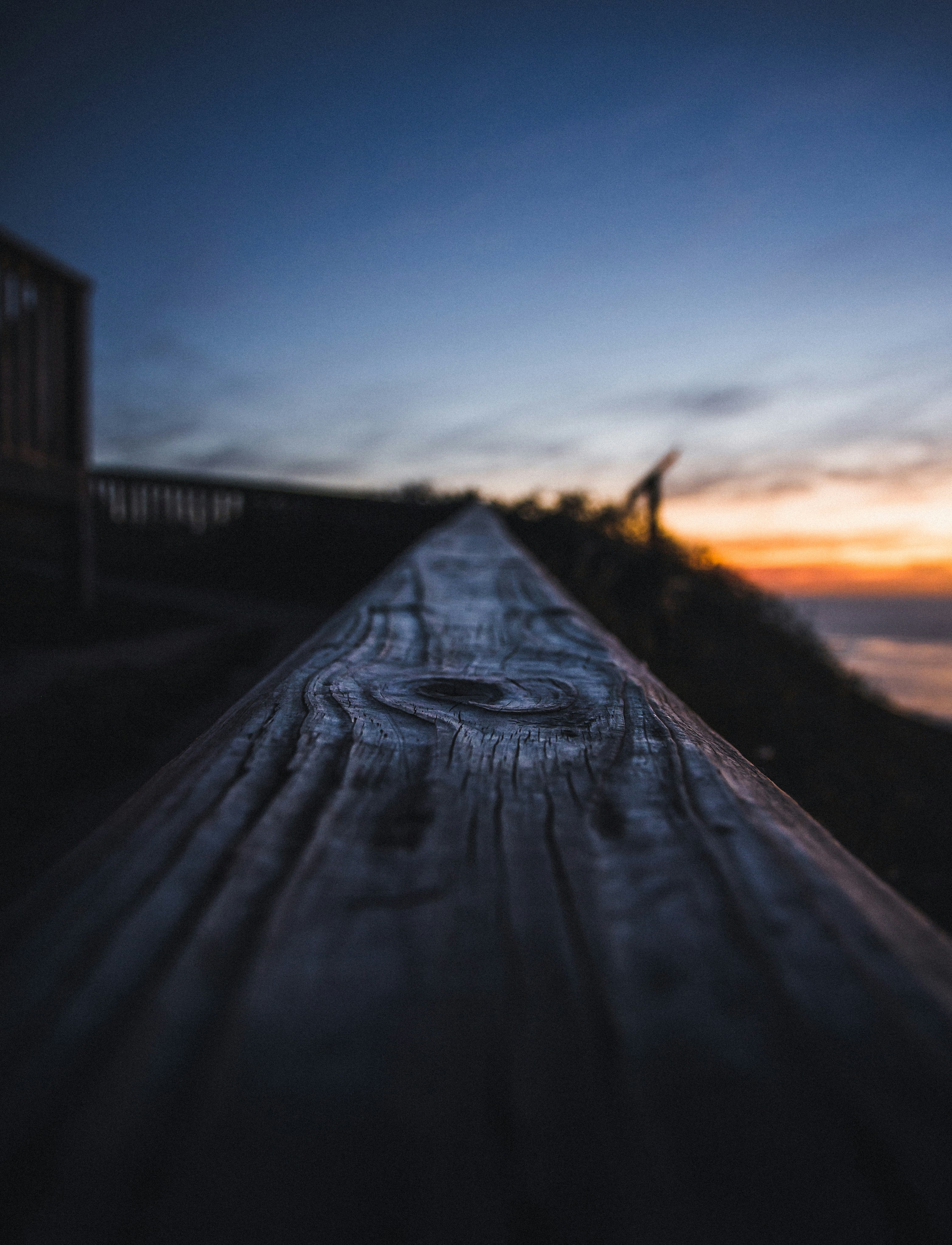 Weathered wooden railing leading towards a vibrant sunset over the horizon. The composition invites viewers to explore the tranquil scene.