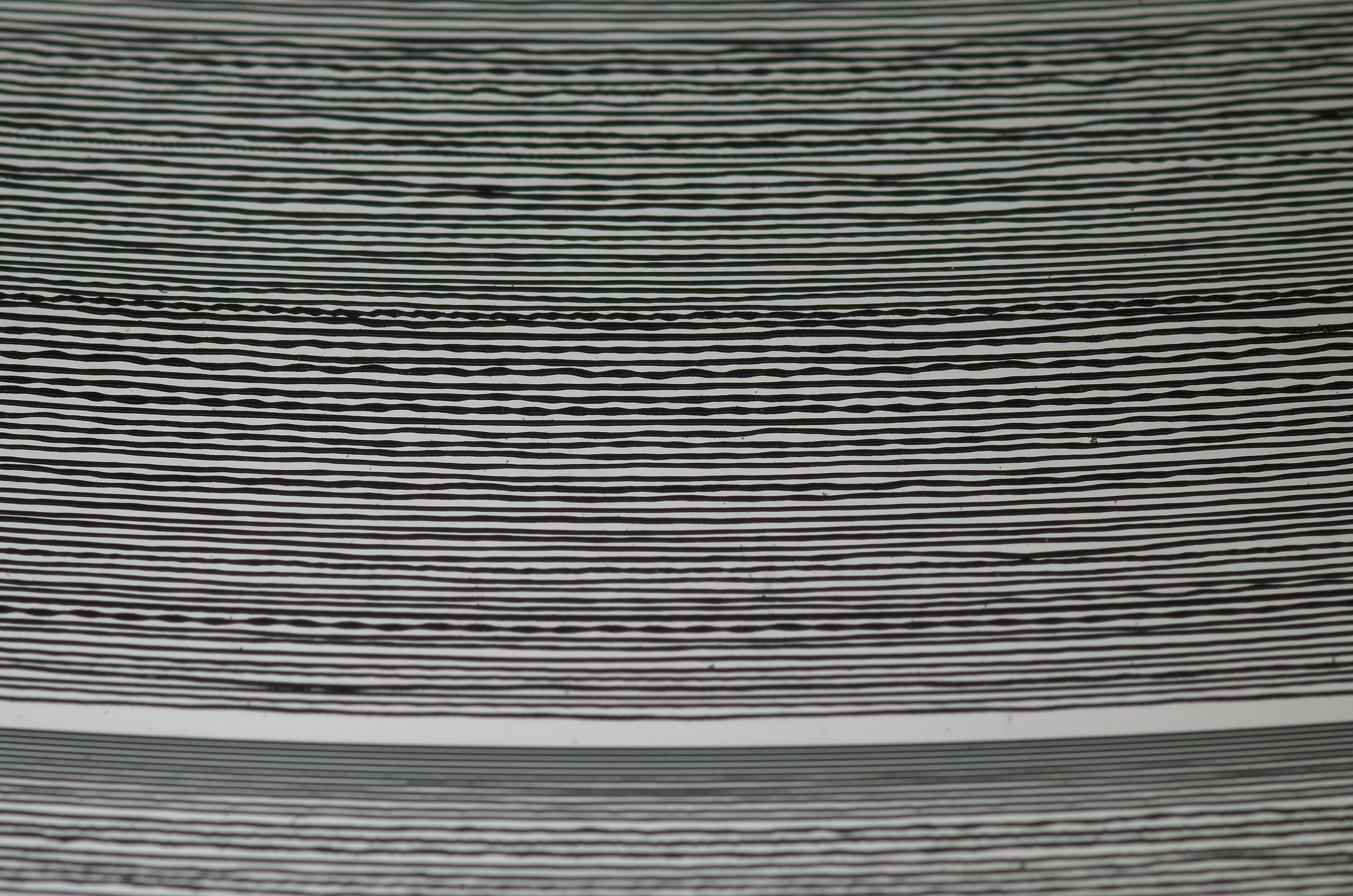 Extreme close-up of a grooved surface with dense parallel lines and a pale mid-band running across the frame.