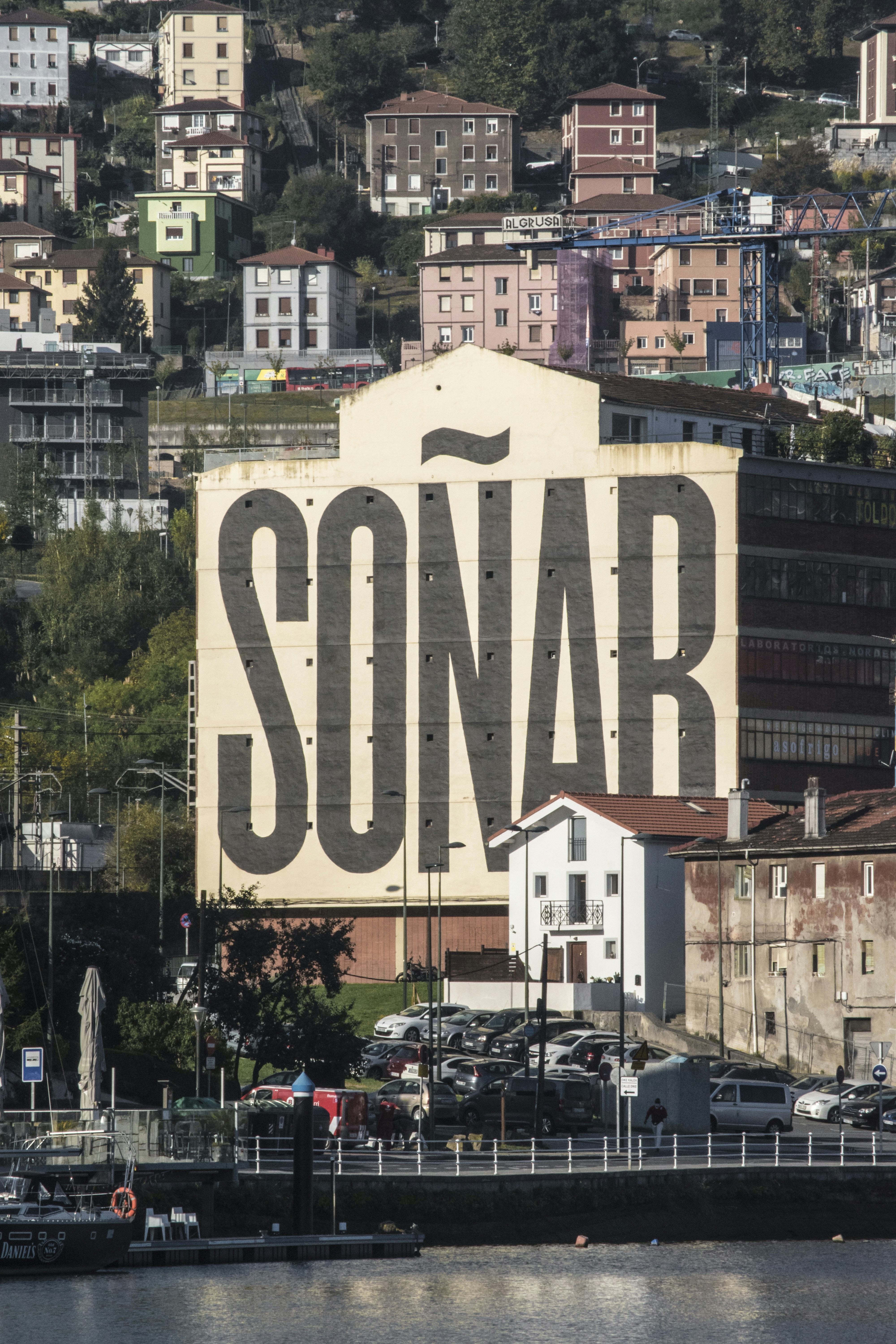 Large mural featuring the word 'SOÑAR' on a building, surrounded by urban architecture and greenery. The scene captures the interplay of art and city life.