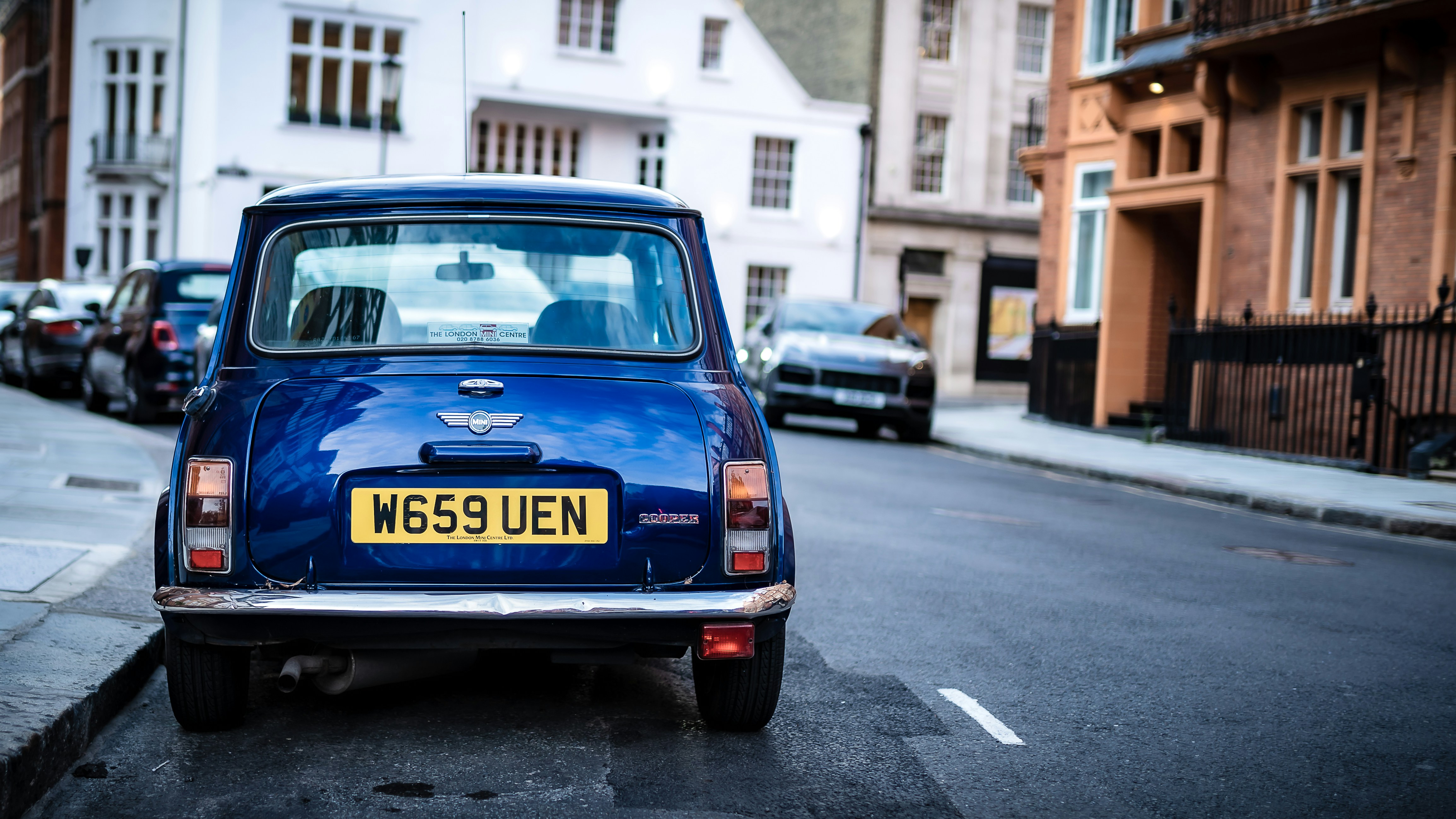 Vintage blue Mini Cooper parked on an urban street lined with historic buildings.