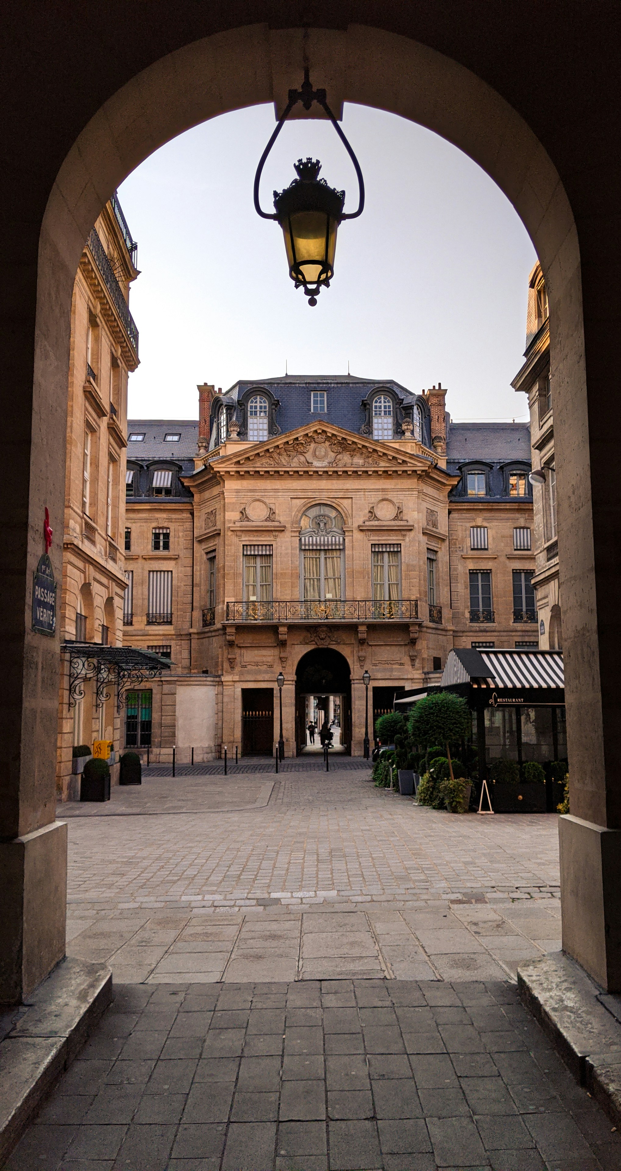 Historic architecture framed by an archway, revealing a tranquil courtyard with lush greenery and cobblestone paths.