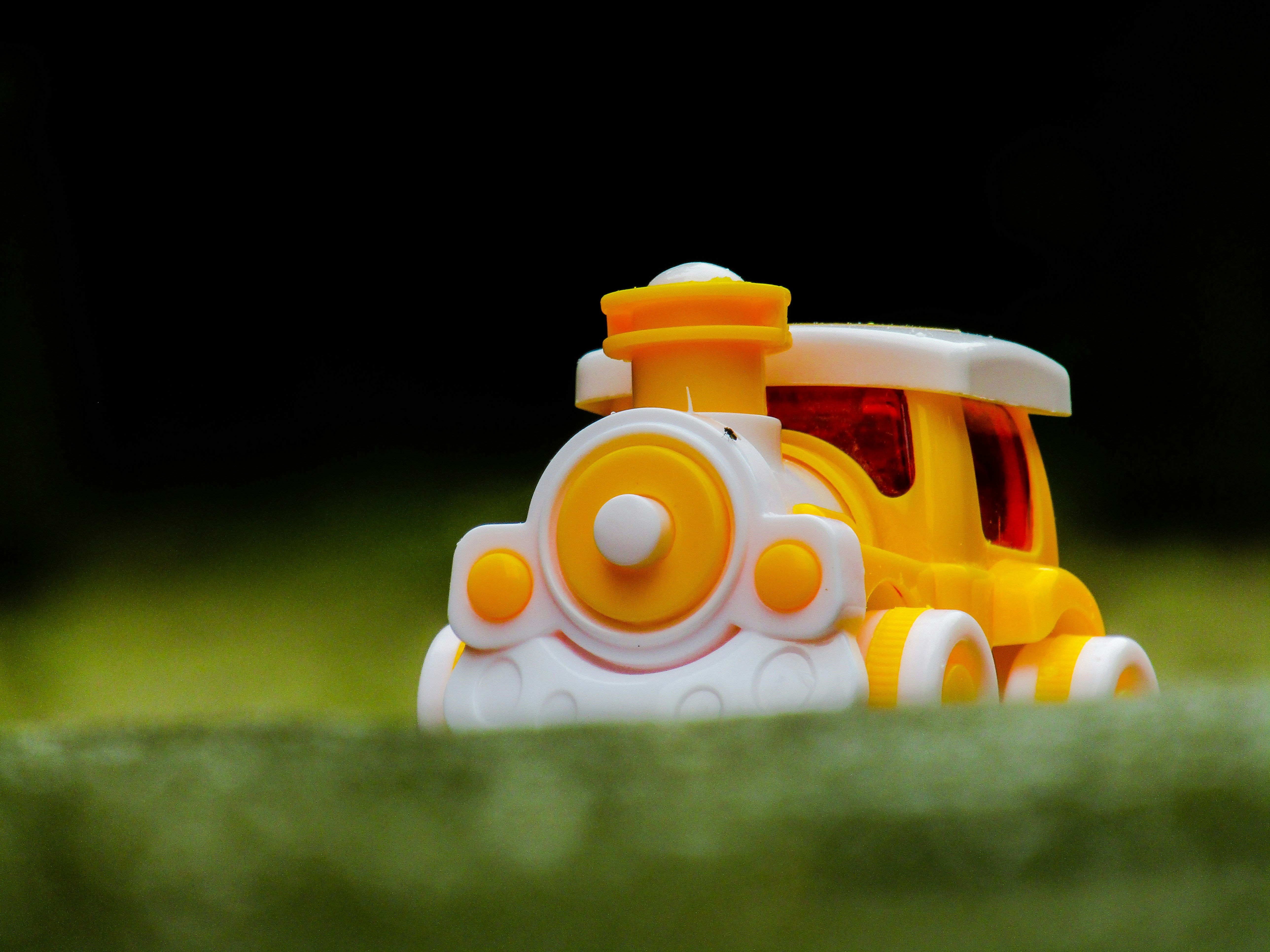 Bright yellow toy train rests on a soft green surface, evoking a sense of playful nostalgia. The blurred background enhances the train's vibrant colors.