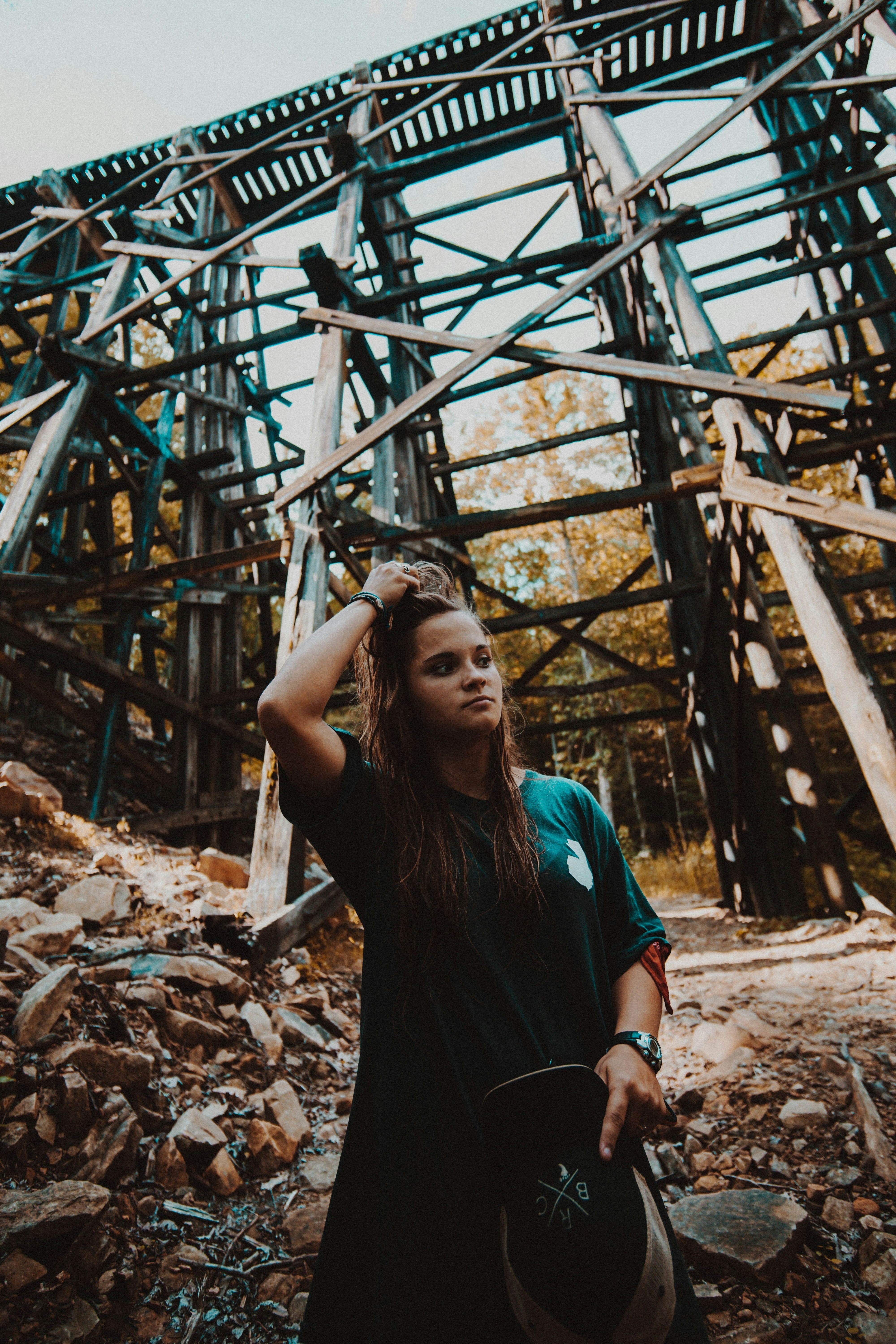 A young woman stands thoughtfully amidst the ruins of a dilapidated wooden structure, framed by vibrant autumn foliage.