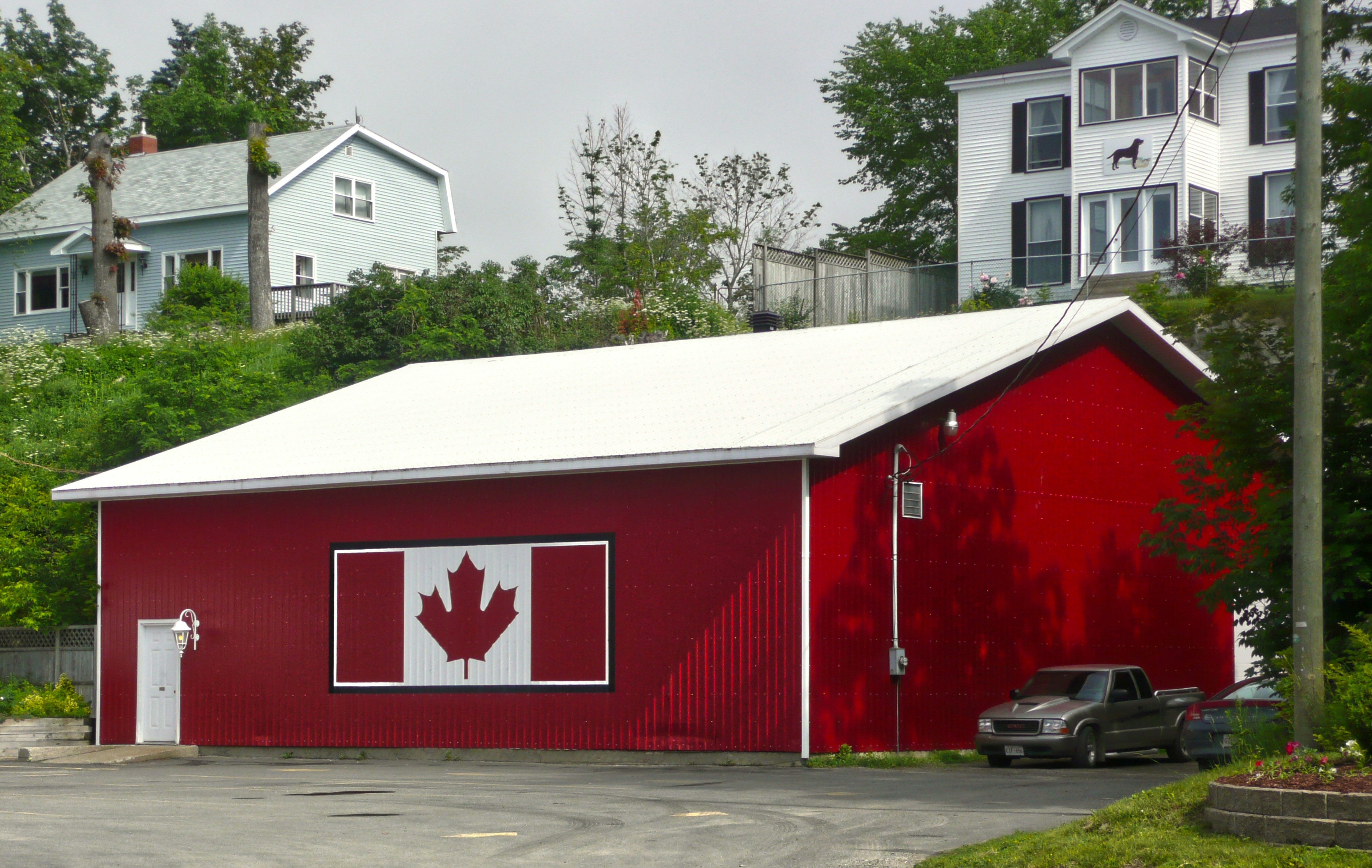 Red barn with a large Canadian flag painted on the side, set against a background of residential houses and trees.
