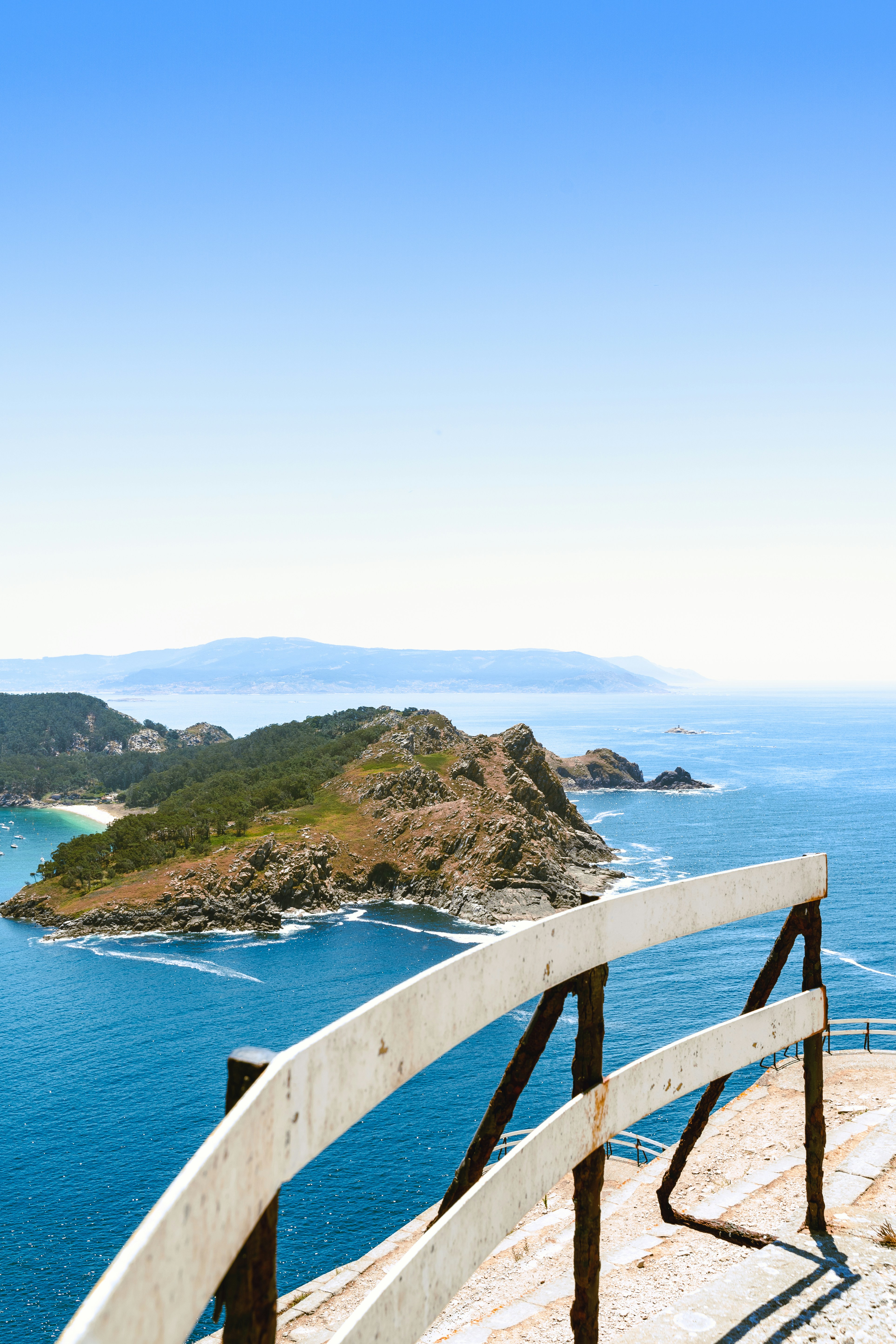 Rustic railing overlooking a tranquil coastal landscape with lush greenery and azure waters, highlighting the beauty of nature's palette.