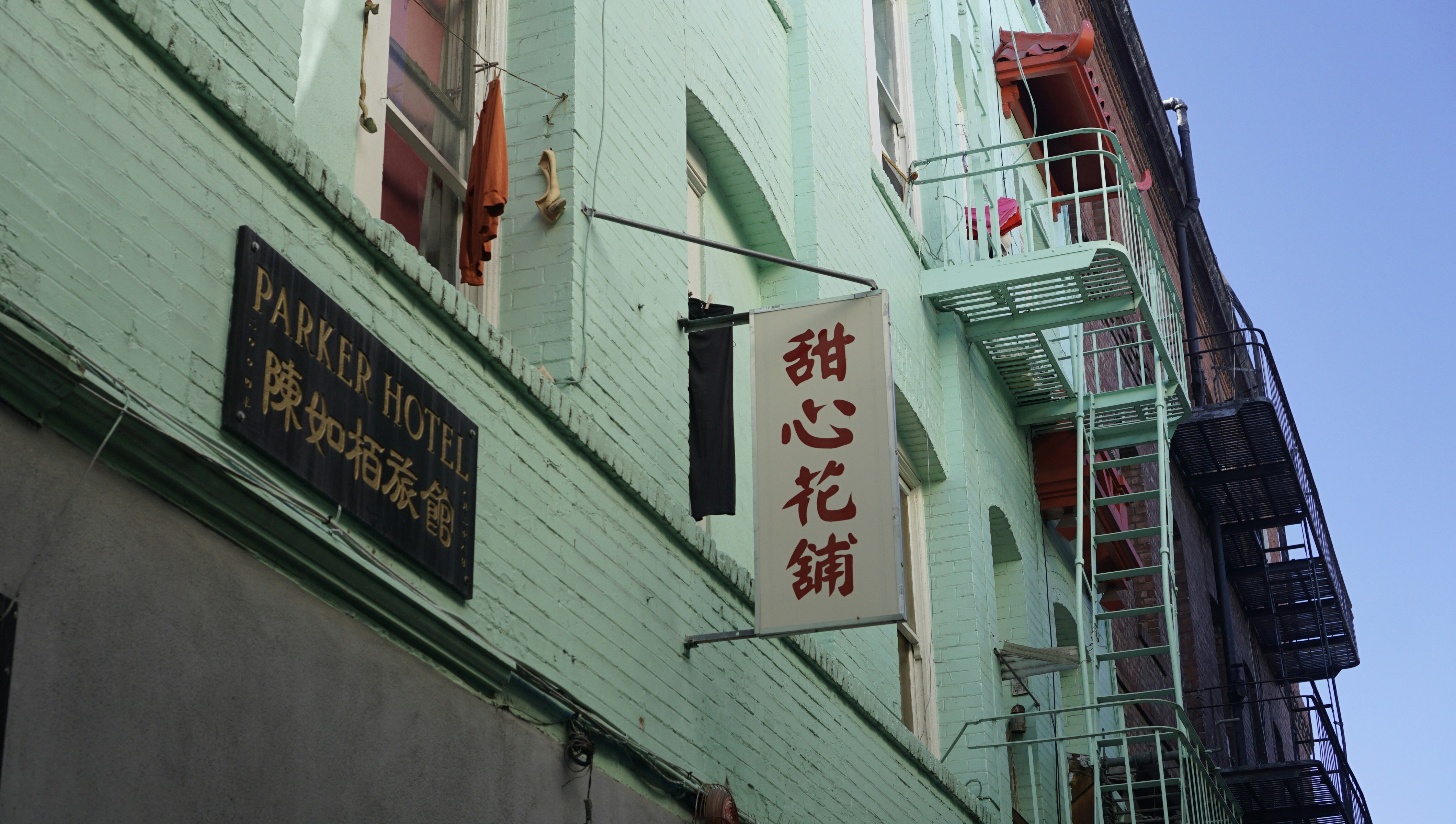 A vintage hotel sign hangs against a pastel green building, showcasing a blend of cultural influences in an urban setting.