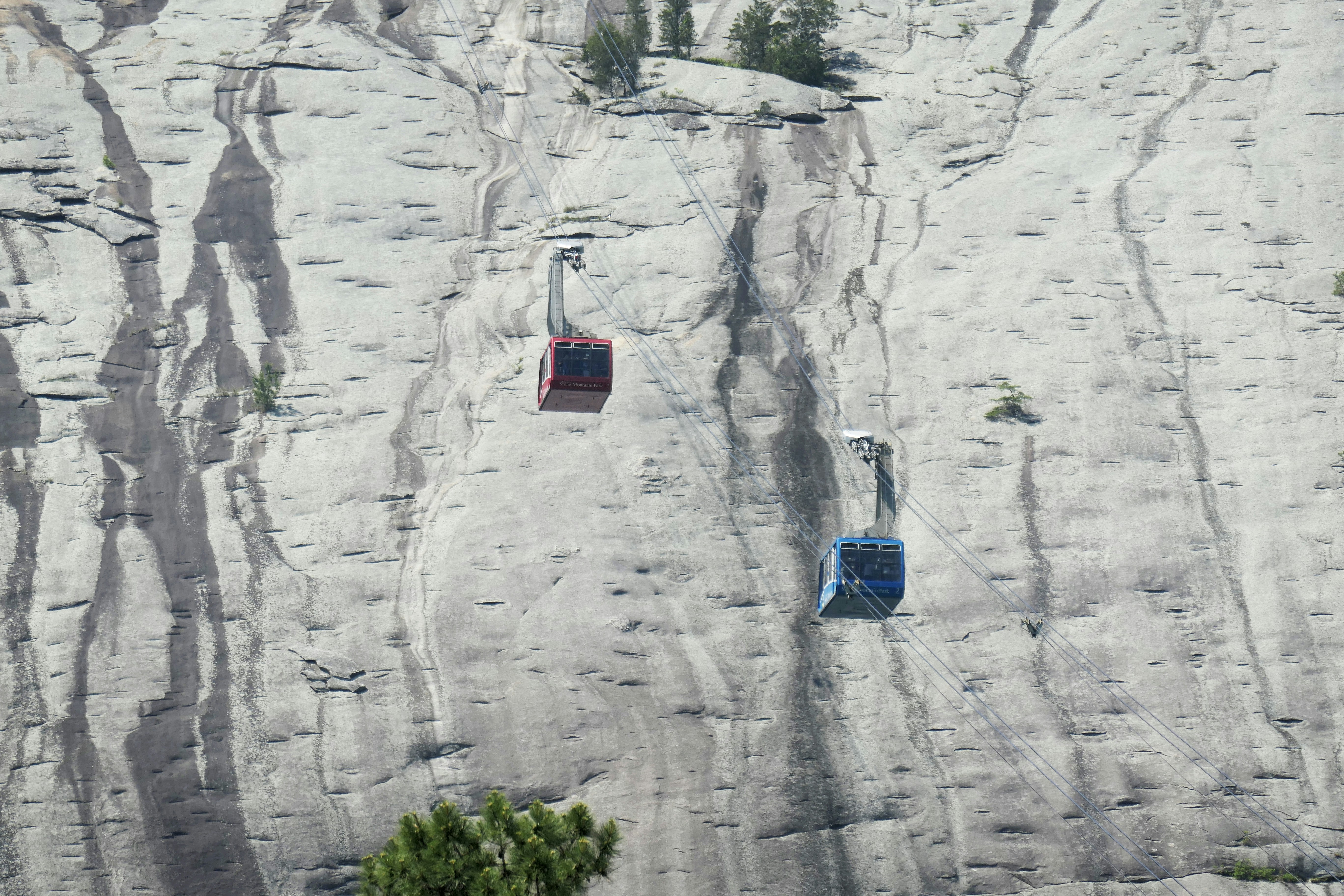 Two gondolas traverse a smooth granite surface, showcasing the contrast of vibrant colors against a natural backdrop. The scene captures the essence of adventure and exploration.