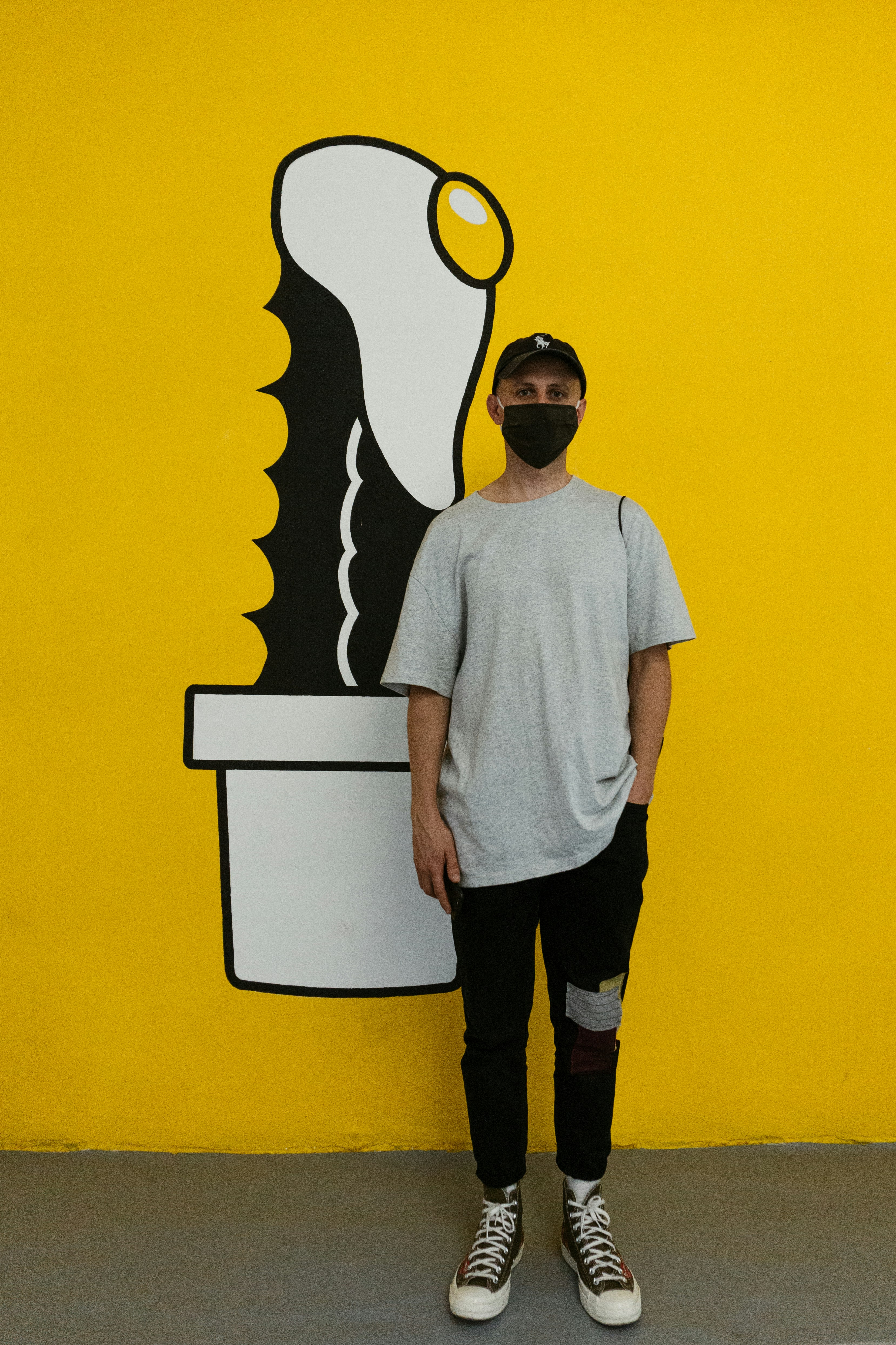 man in white crew neck t-shirt and black pants standing beside yellow wall