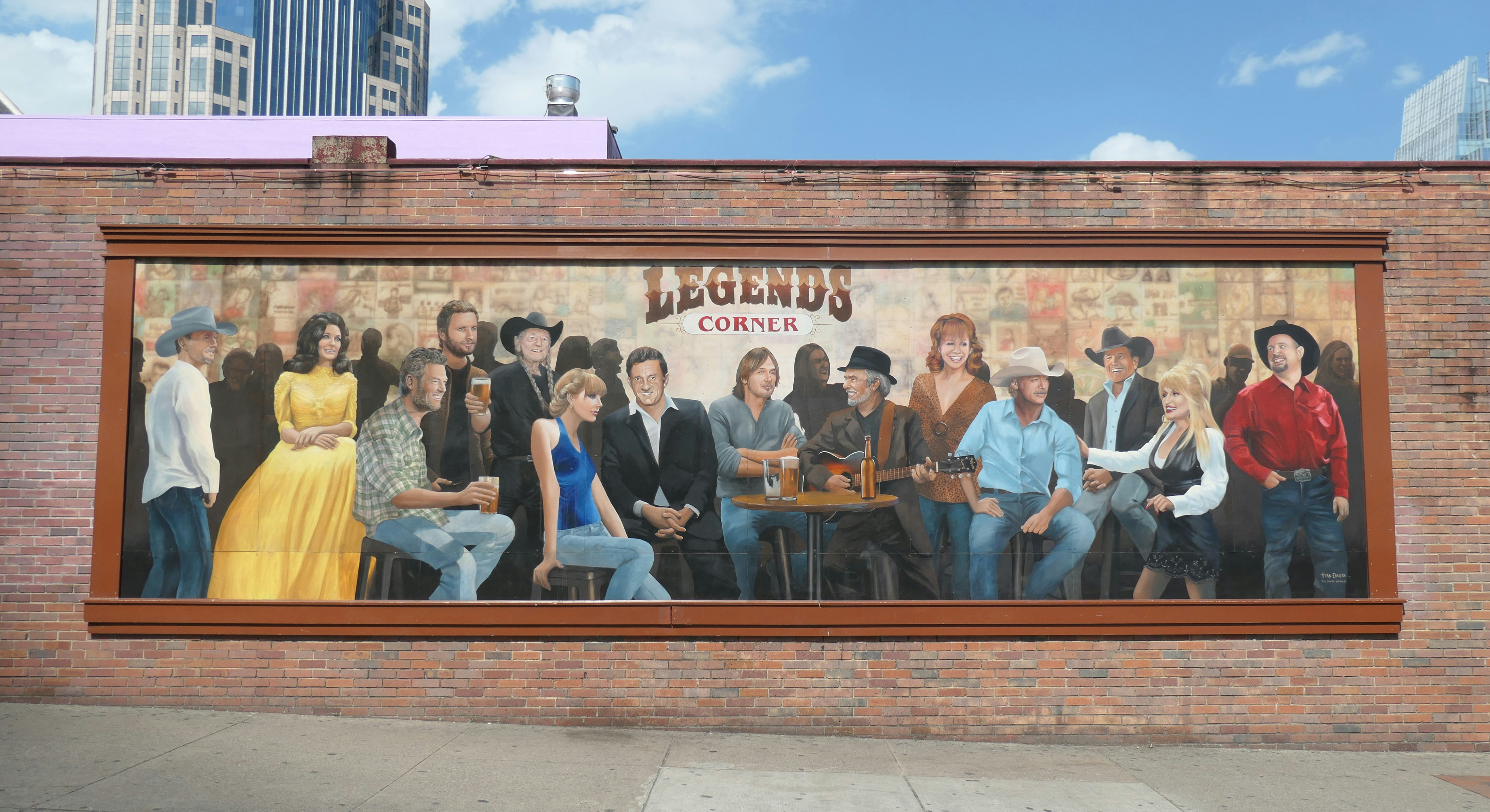 Mural of diverse individuals seated and standing around a table on a brick wall under a clear sky.