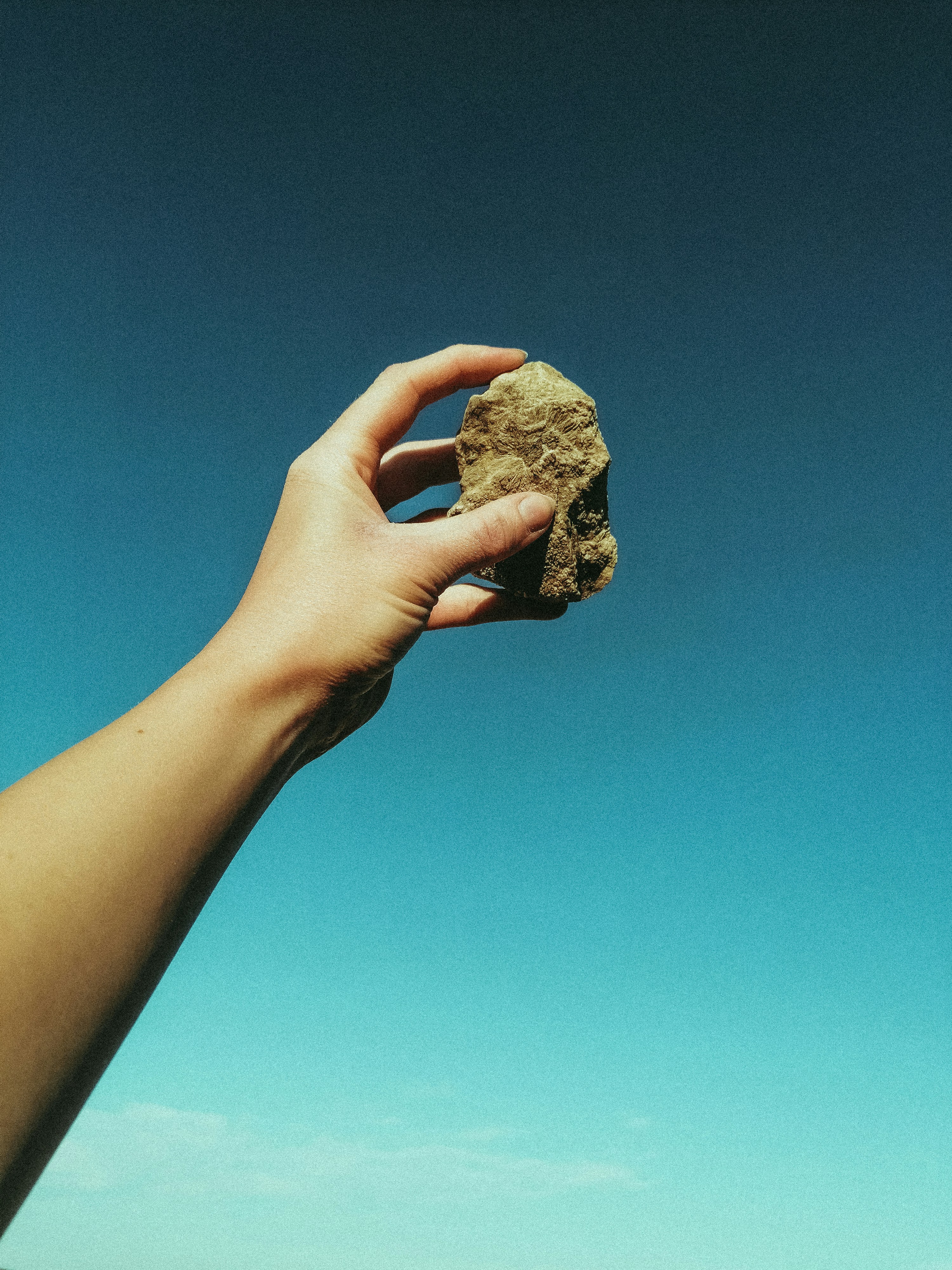 A hand holds a textured rock against a clear blue sky, symbolizing a bond with nature.