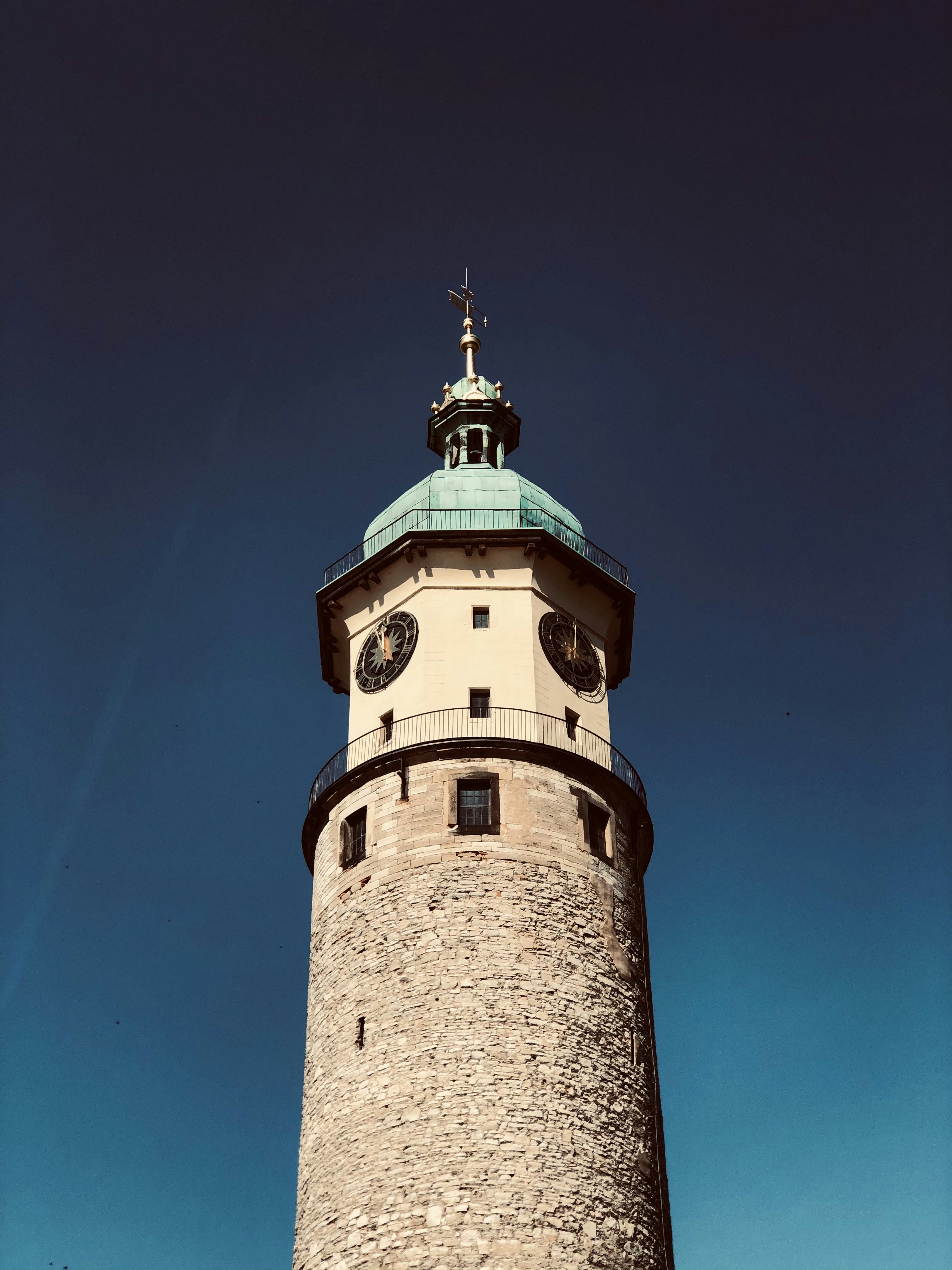 Historic clock tower with a green copper dome and intricate clock faces against a clear blue sky.