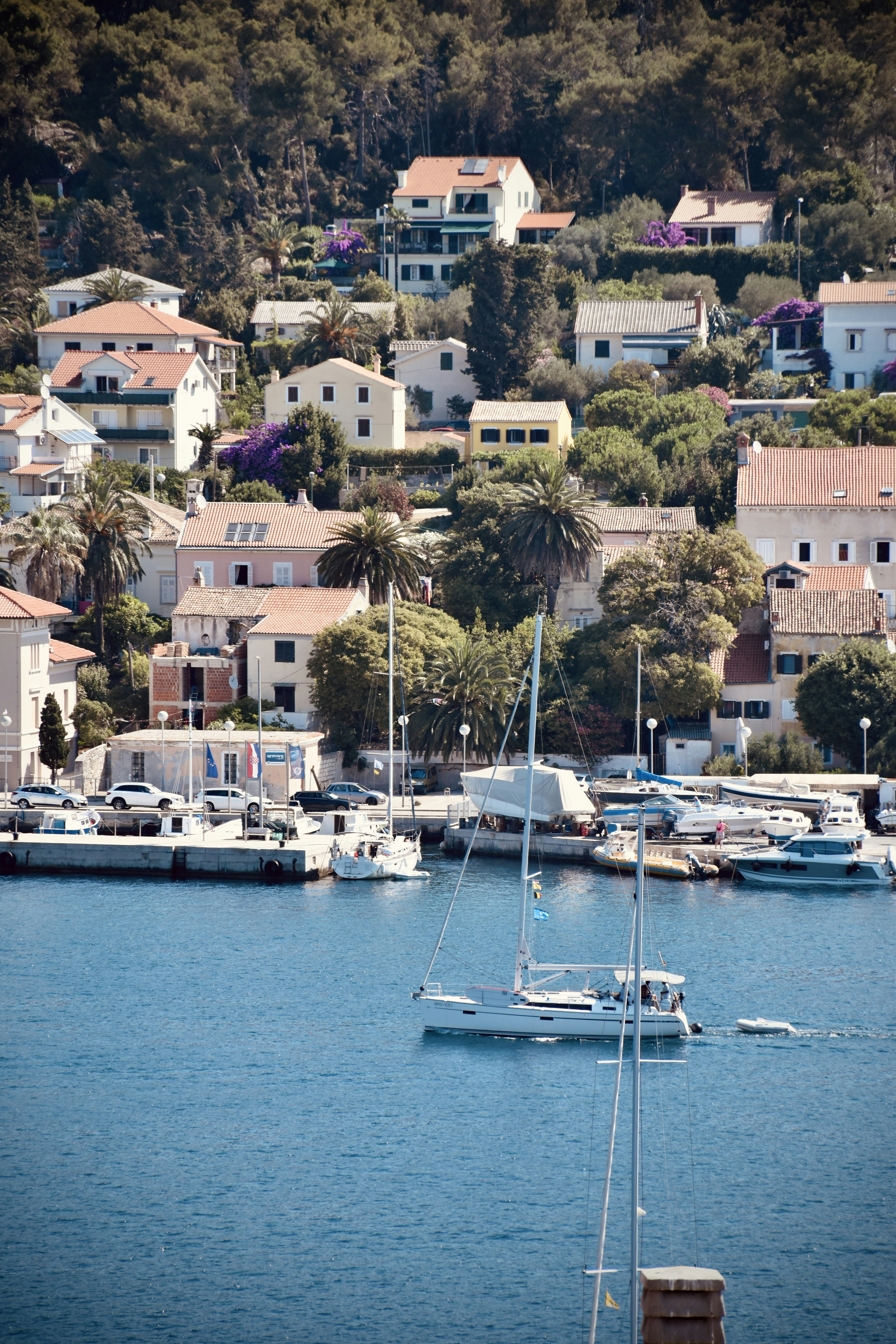 White sailboat gliding through the port with colorful hillside houses in the background.
