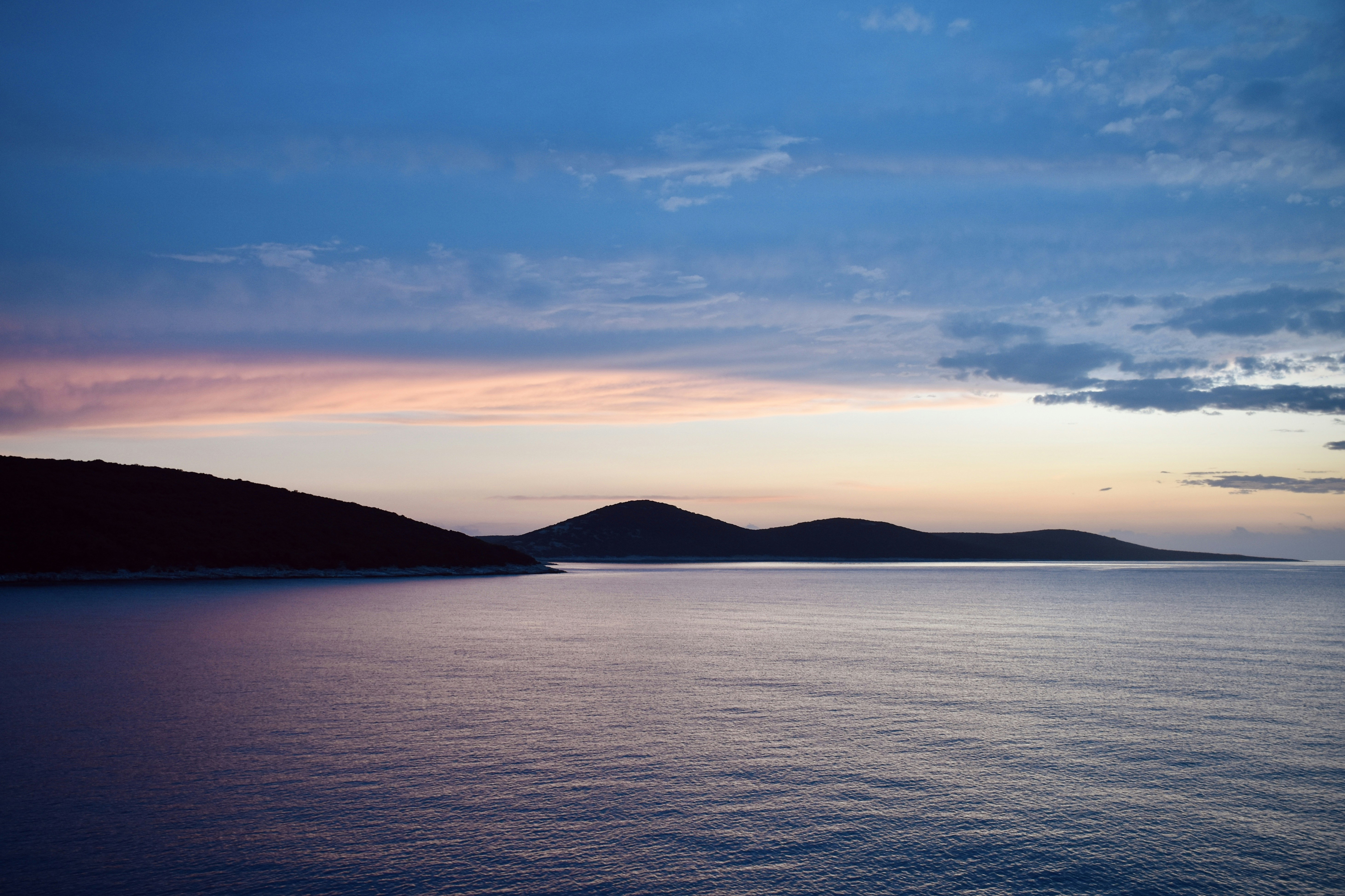 Serene sea with silhouetted islands under a vibrant post-sunset sky.