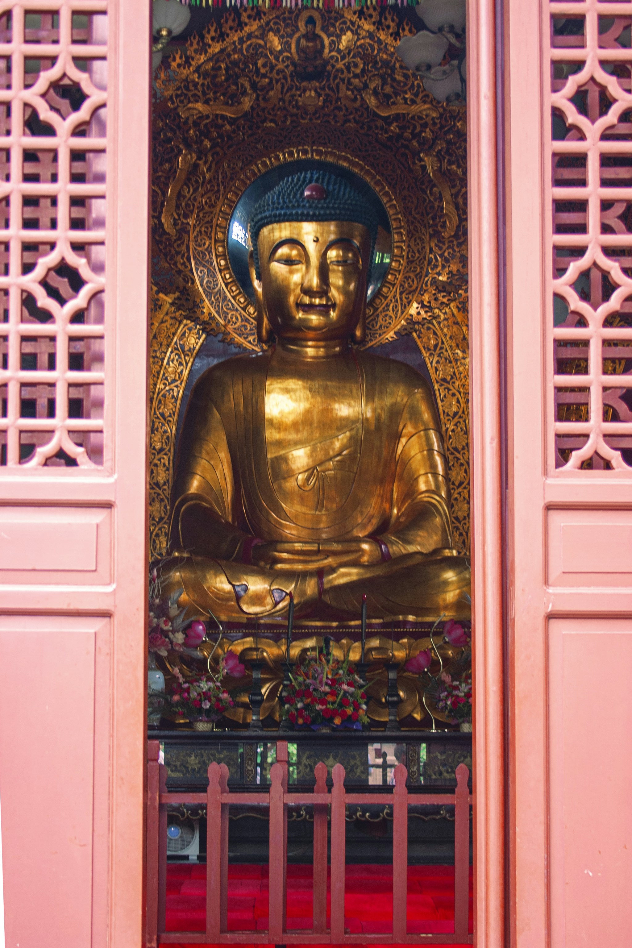 Golden Buddha statue seated within ornate temple structure, framed by decorative doors. A serene atmosphere invites contemplation.
