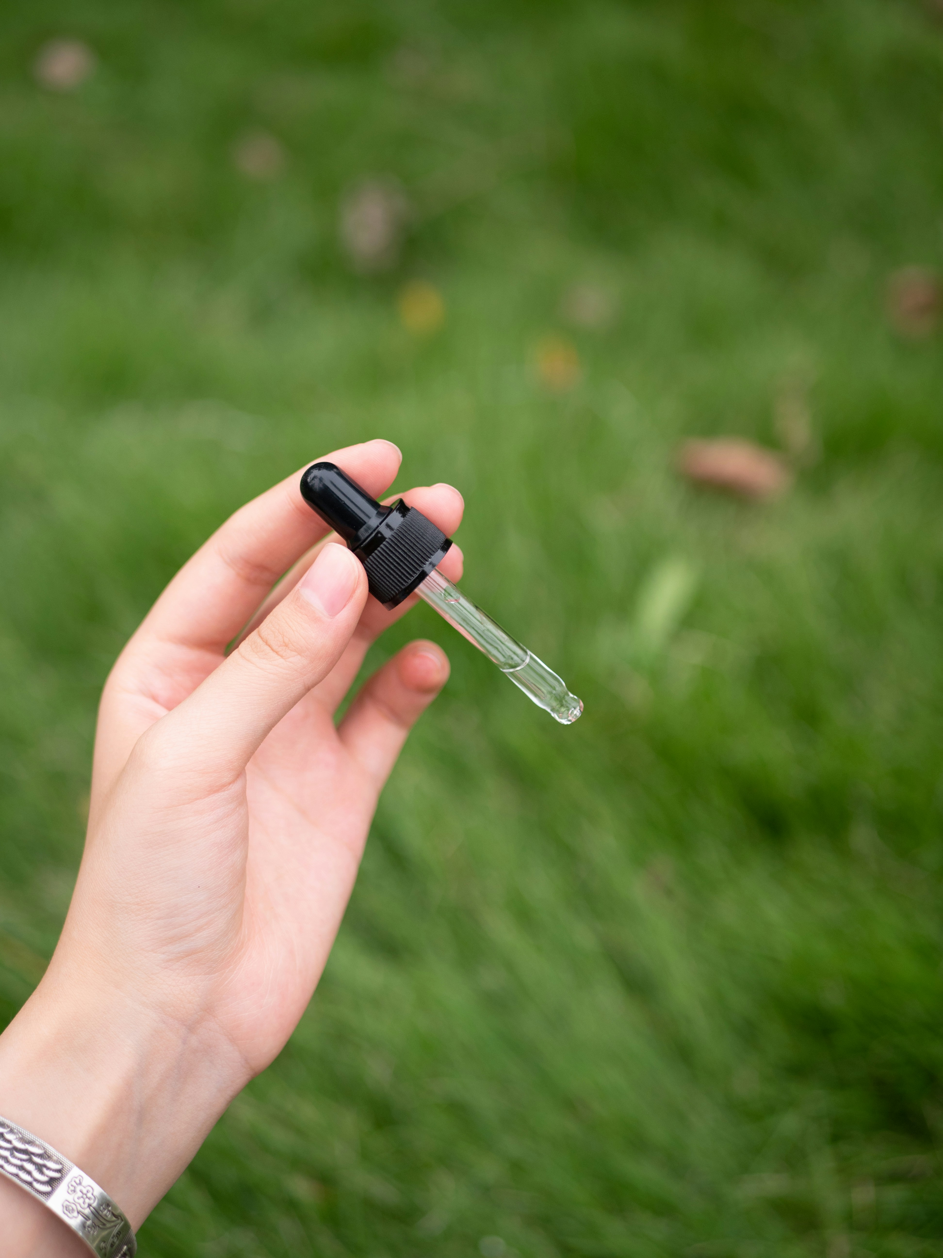 Hand holding a dropper over lush green grass, showcasing the delicate balance of nature and science.