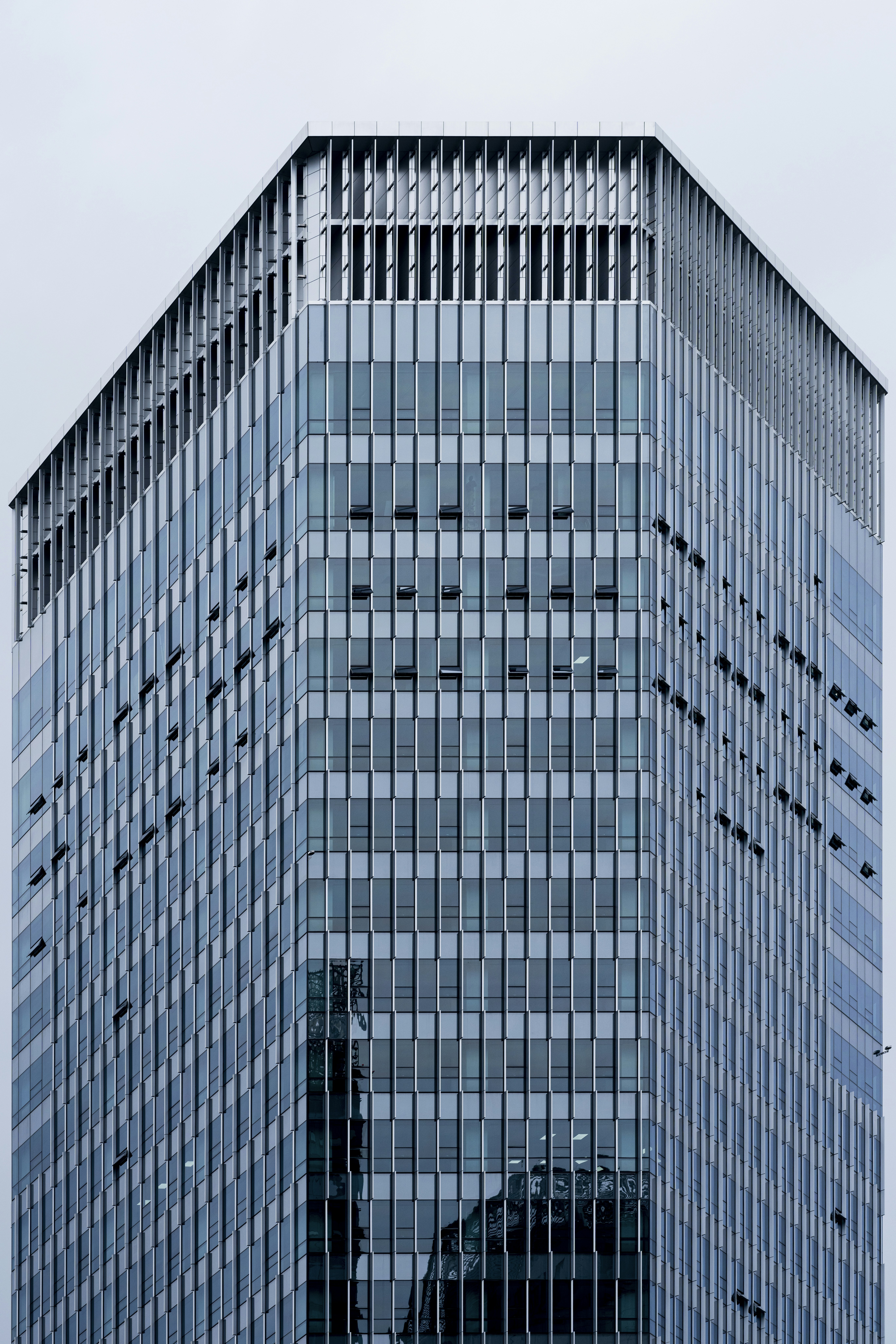 A sleek, glass-clad skyscraper with a distinct angular design, showcasing reflections and patterns against a gray sky.