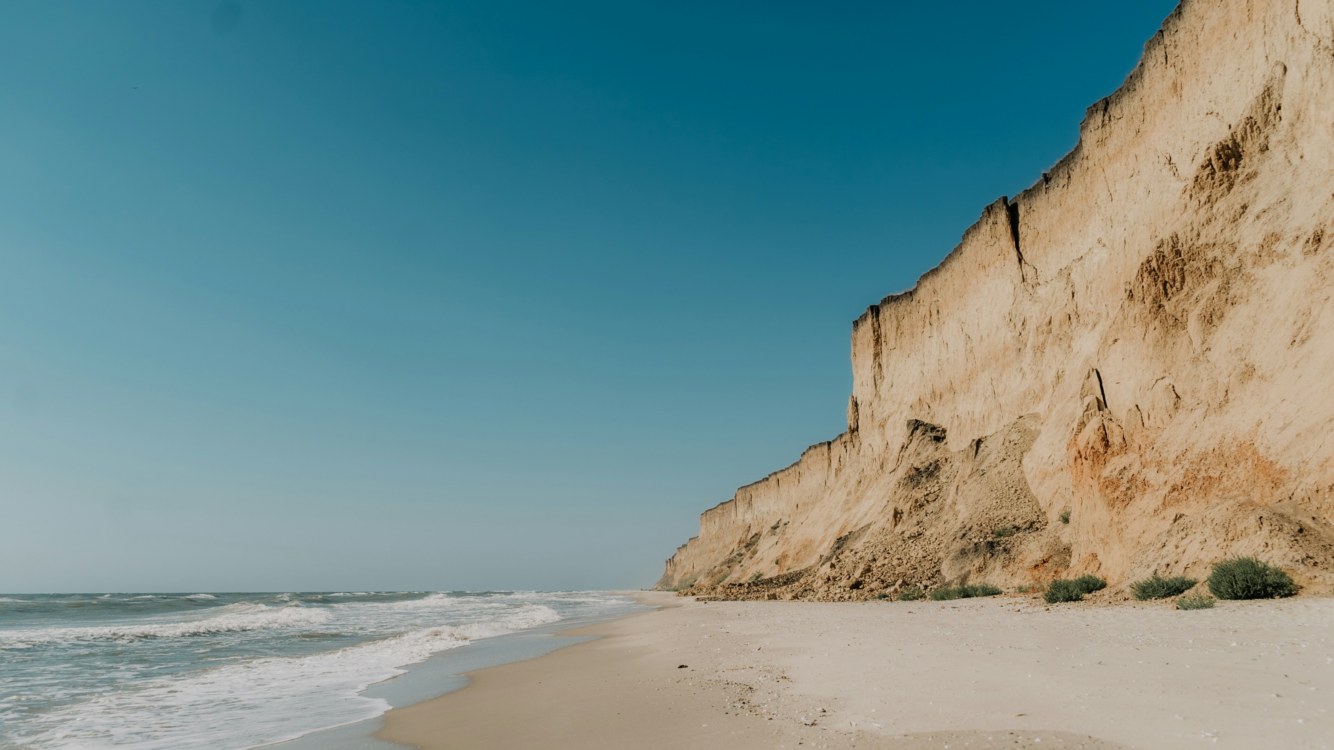 Expansive sandy beach bordered by towering golden cliffs under a clear blue sky.