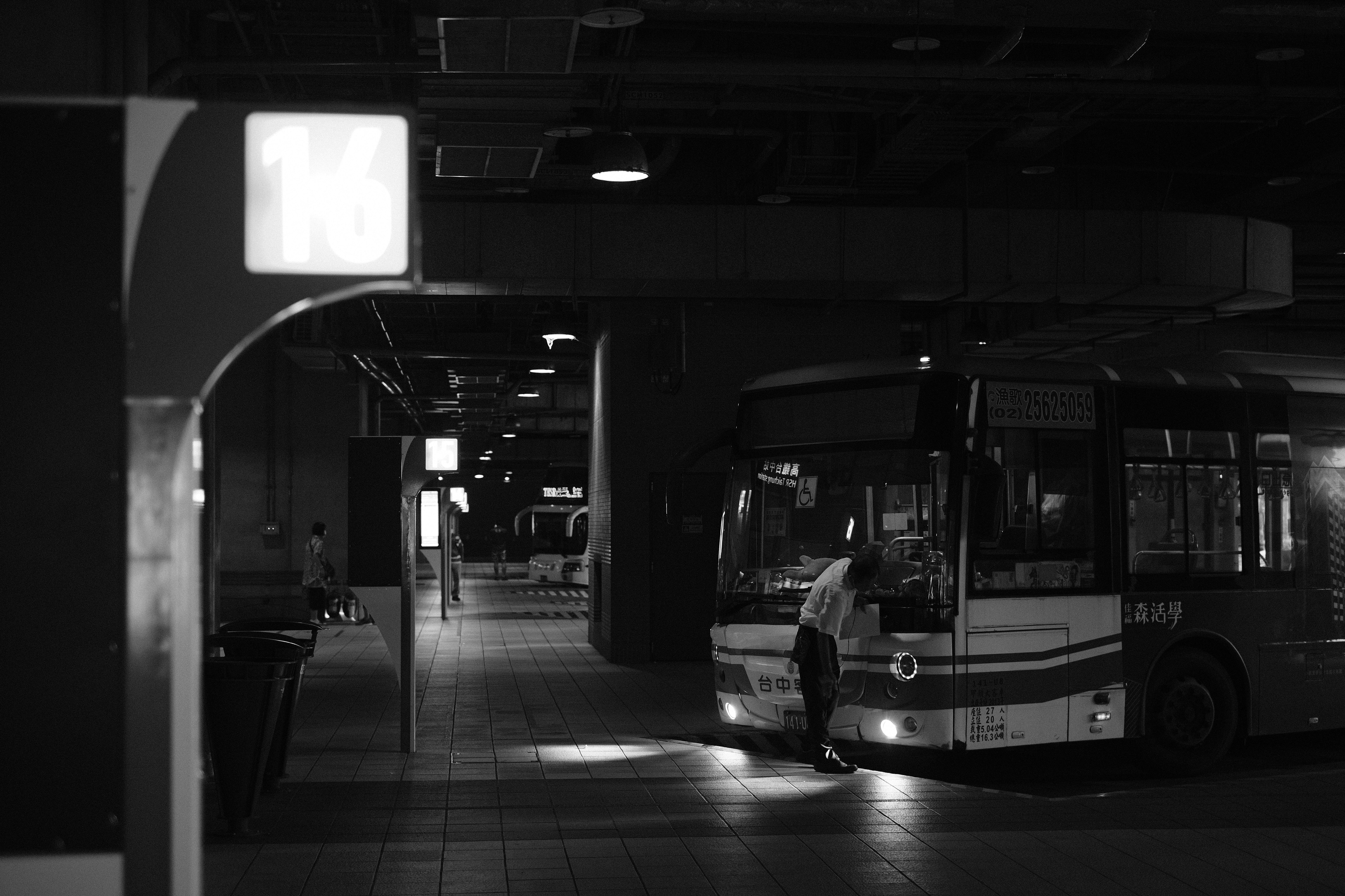 A city bus prepares for departure at a dimly lit station, illuminated by overhead lights and the number 116 sign. The scene captures the essence of urban transit life.