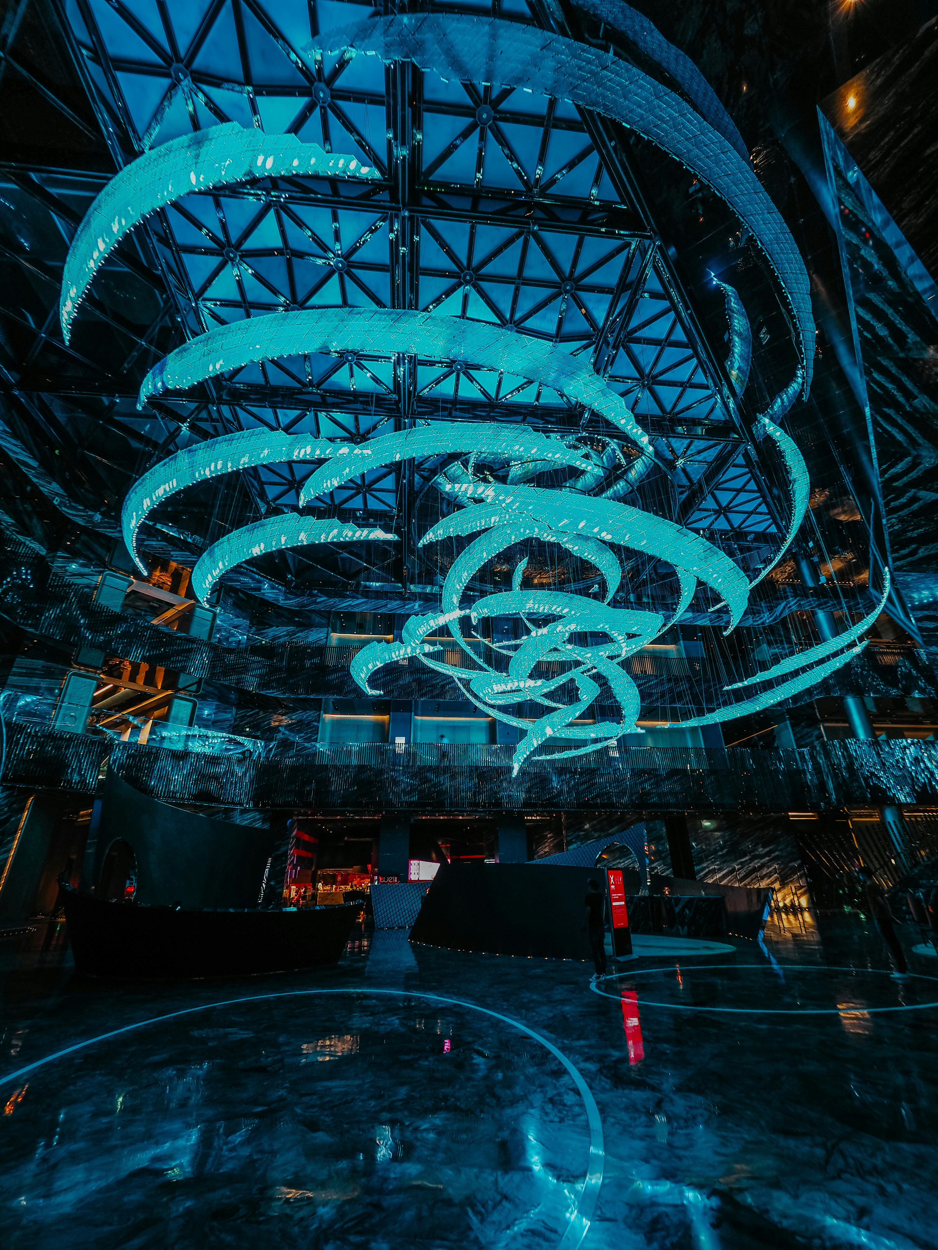 Intricate blue lighting installation suspended in a modern architectural space, reflecting off polished surfaces. 