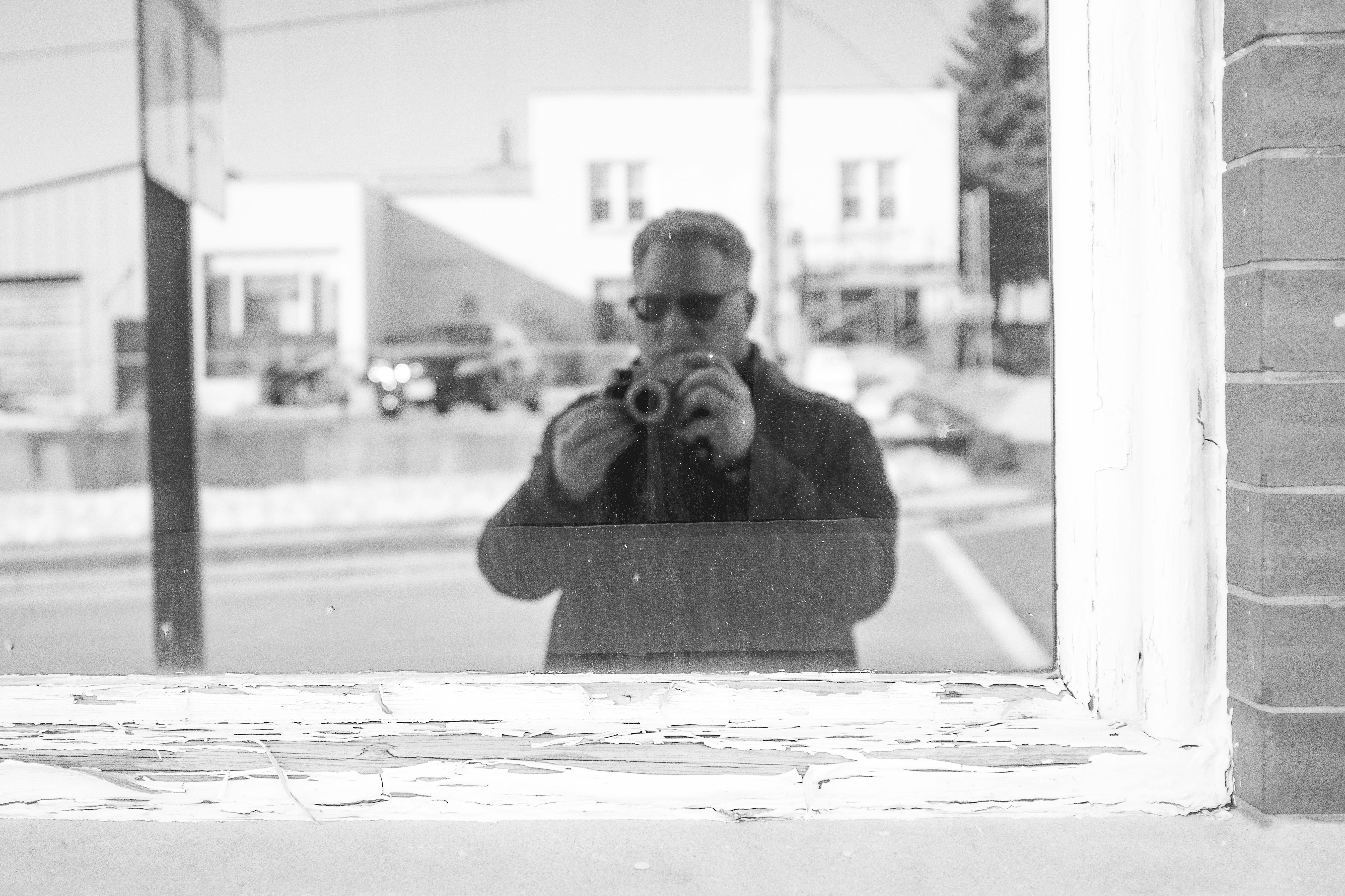 Glassbound Gaze: A Street Photographer Reflected in a Weathered Window
