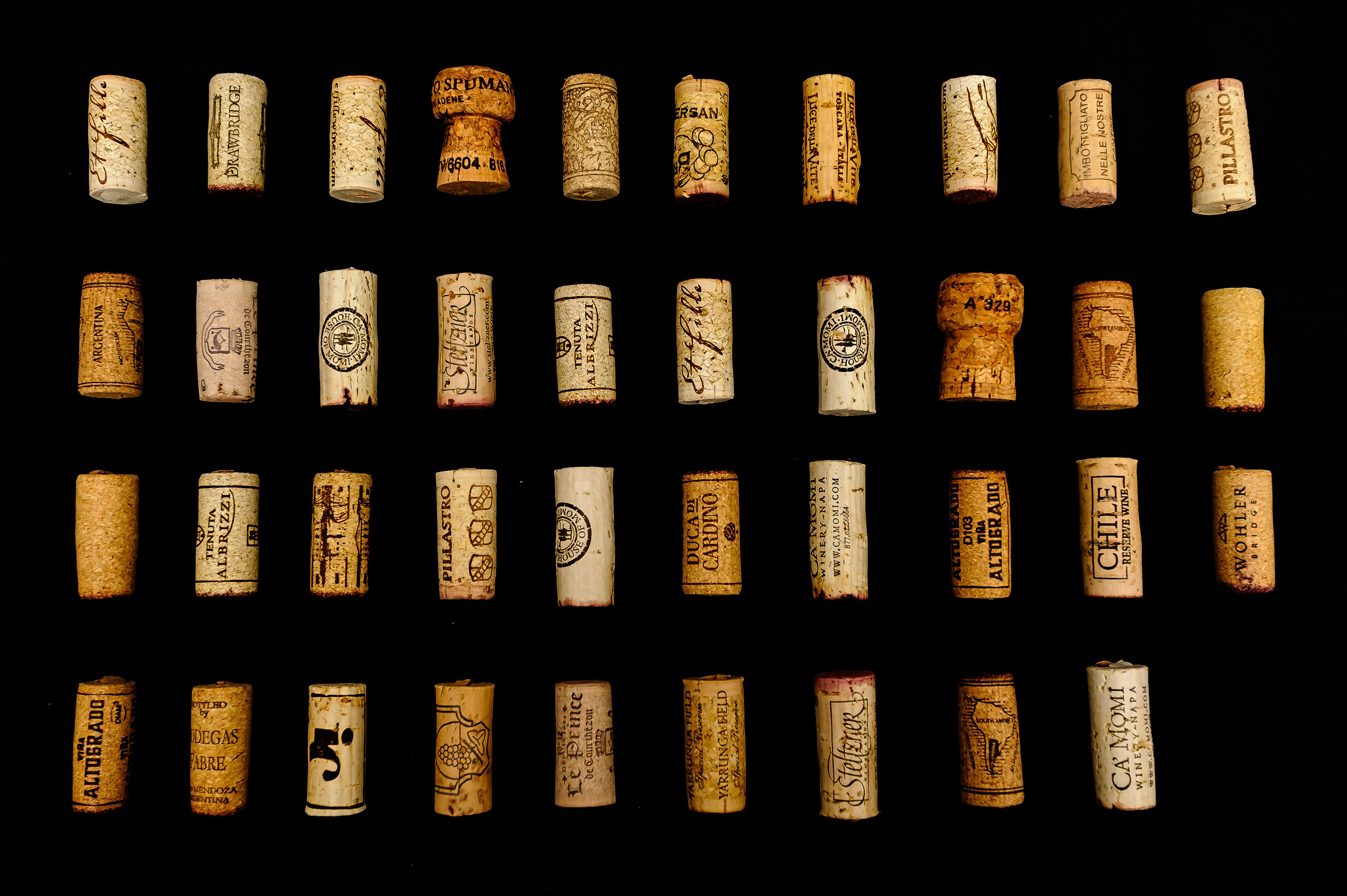 Array of assorted wine corks arranged in neat rows against a black background.