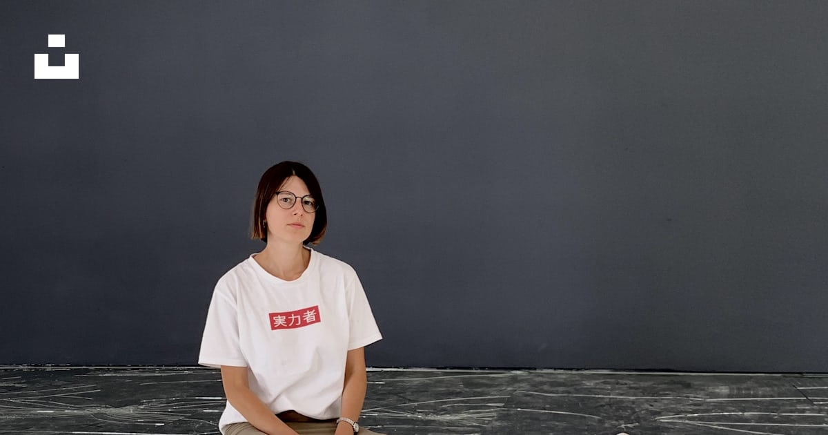 灰色のコンクリートの床に座っている白いtシャツと茶色のスカートの女性の写真 Unsplashのアパレルの無料画像