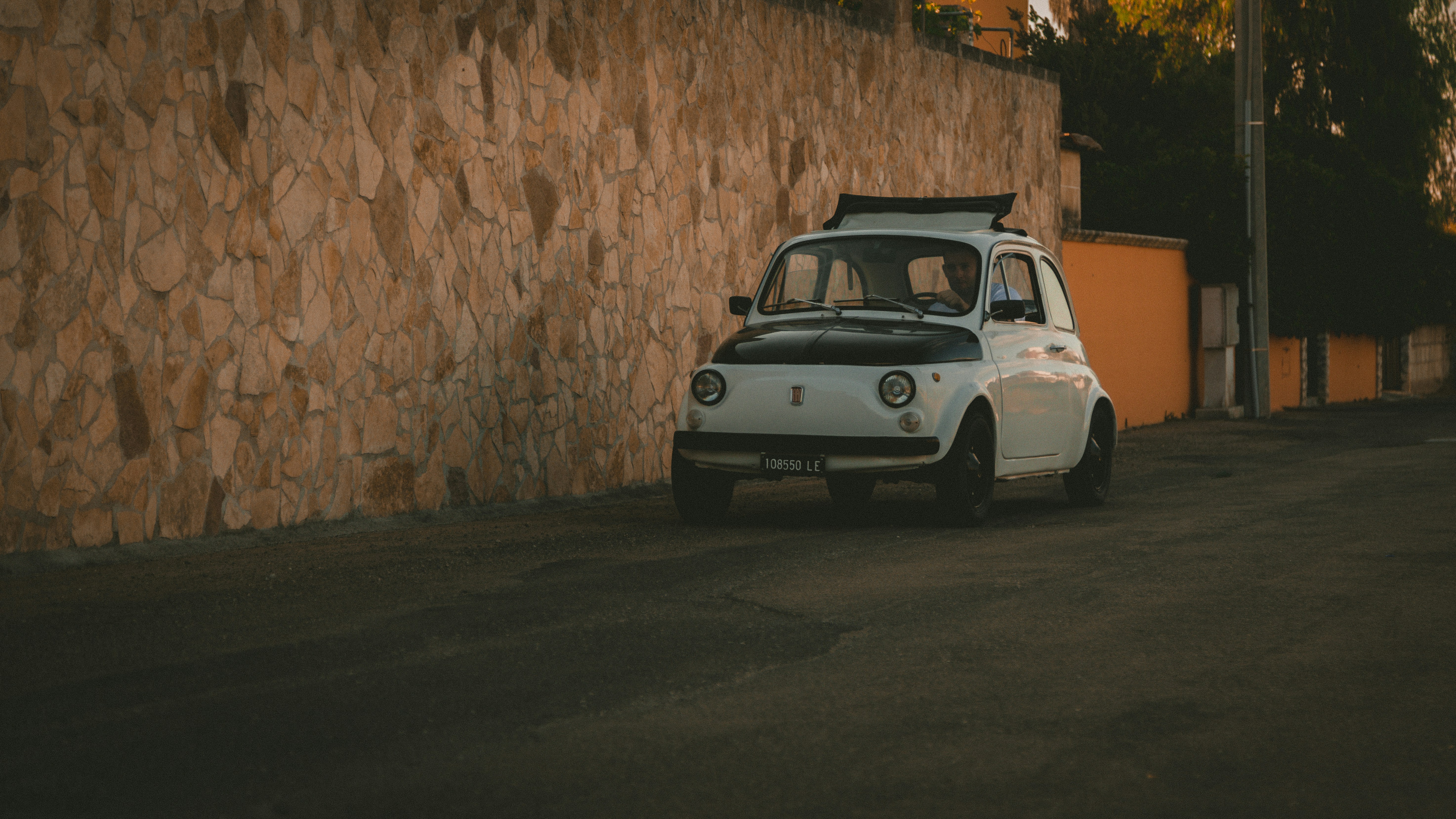 Vintage Fiat 500 parked beside a textured stone wall in soft evening light.