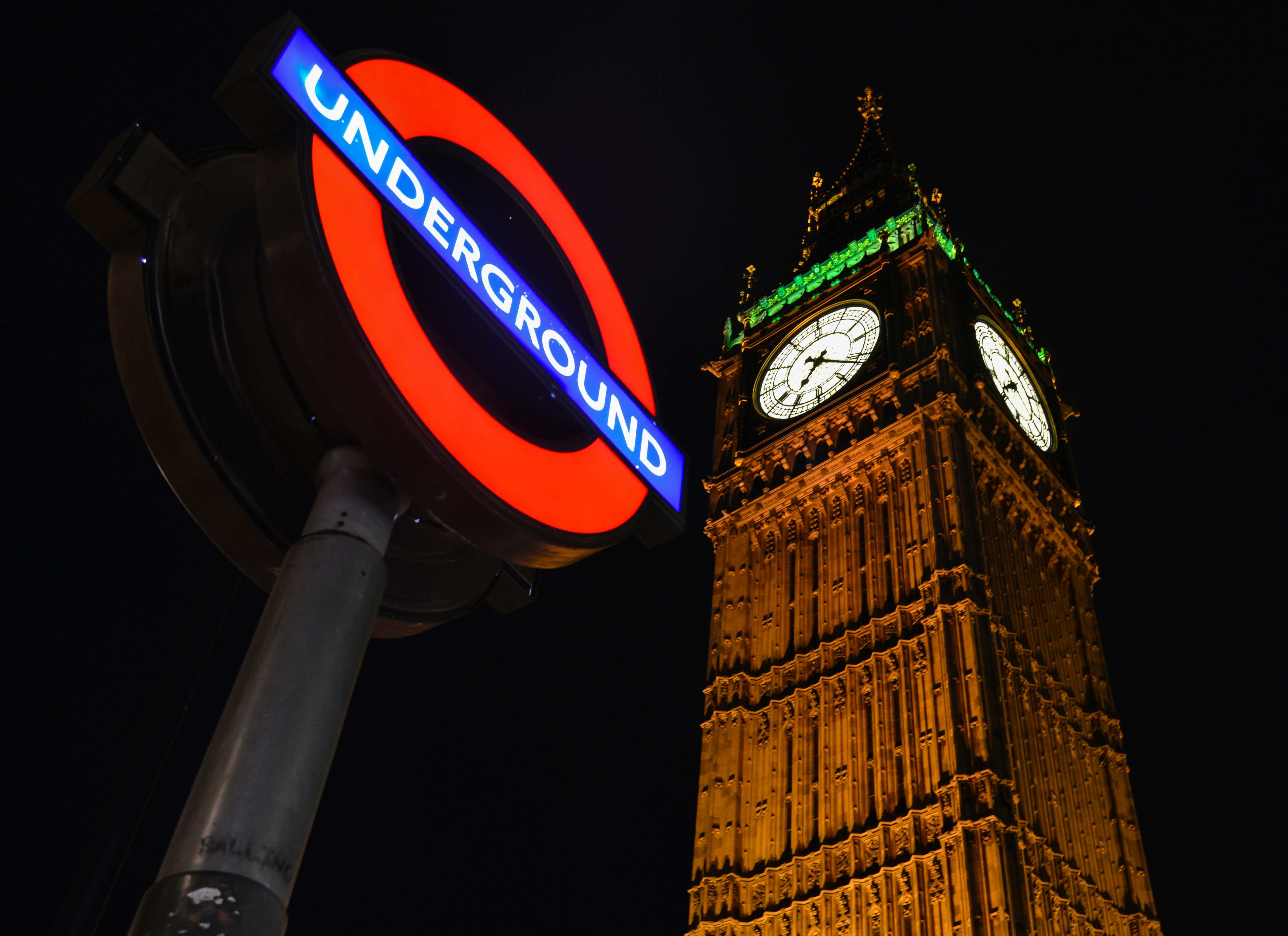 London Underground sign and illuminated clock tower against a night sky.
