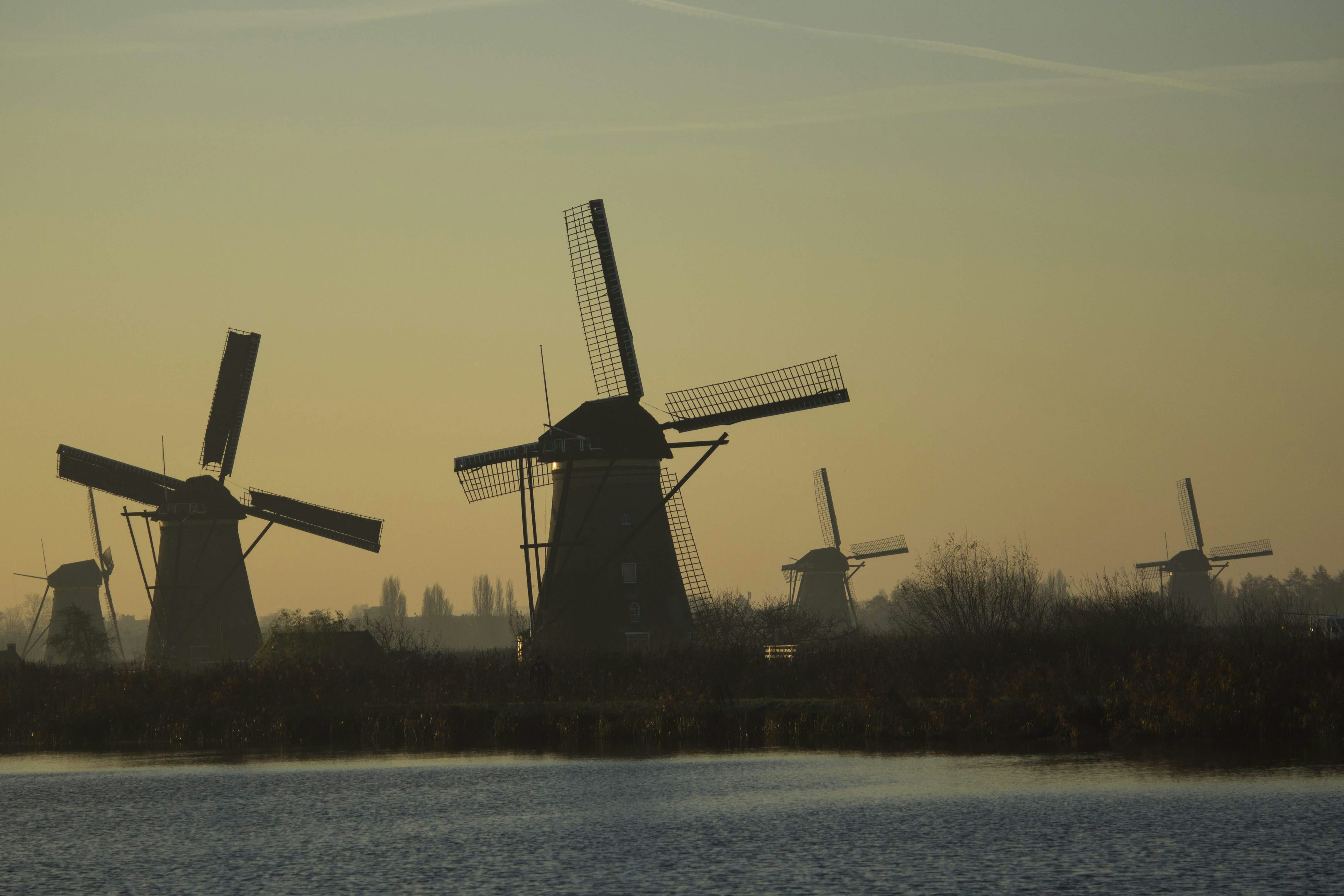 Silhouetted windmills against a soft golden sunrise at Kinderdijk, with a calm body of water in the foreground.