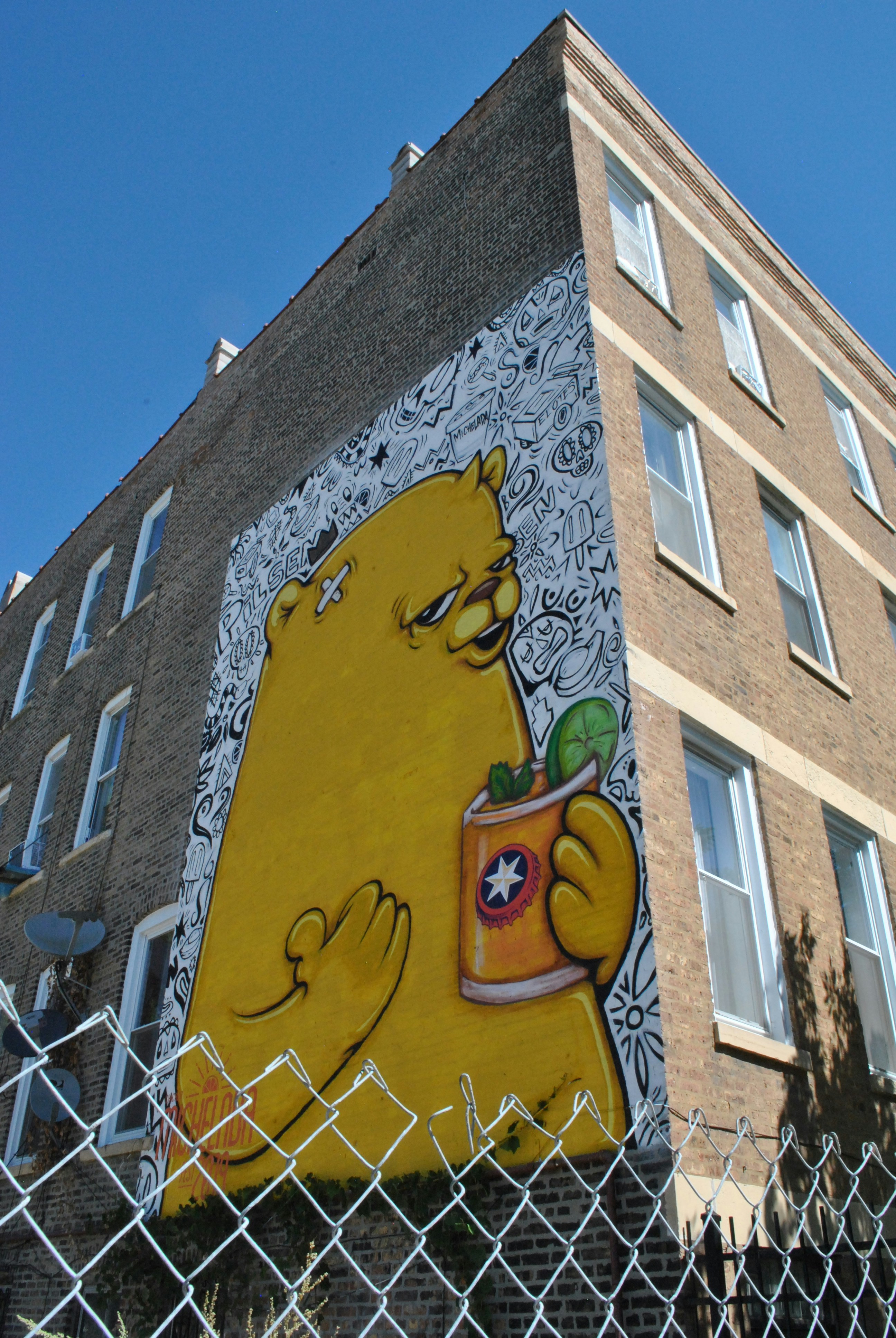 Yellow Bear M mural climbs the brick wall of a sunlit building