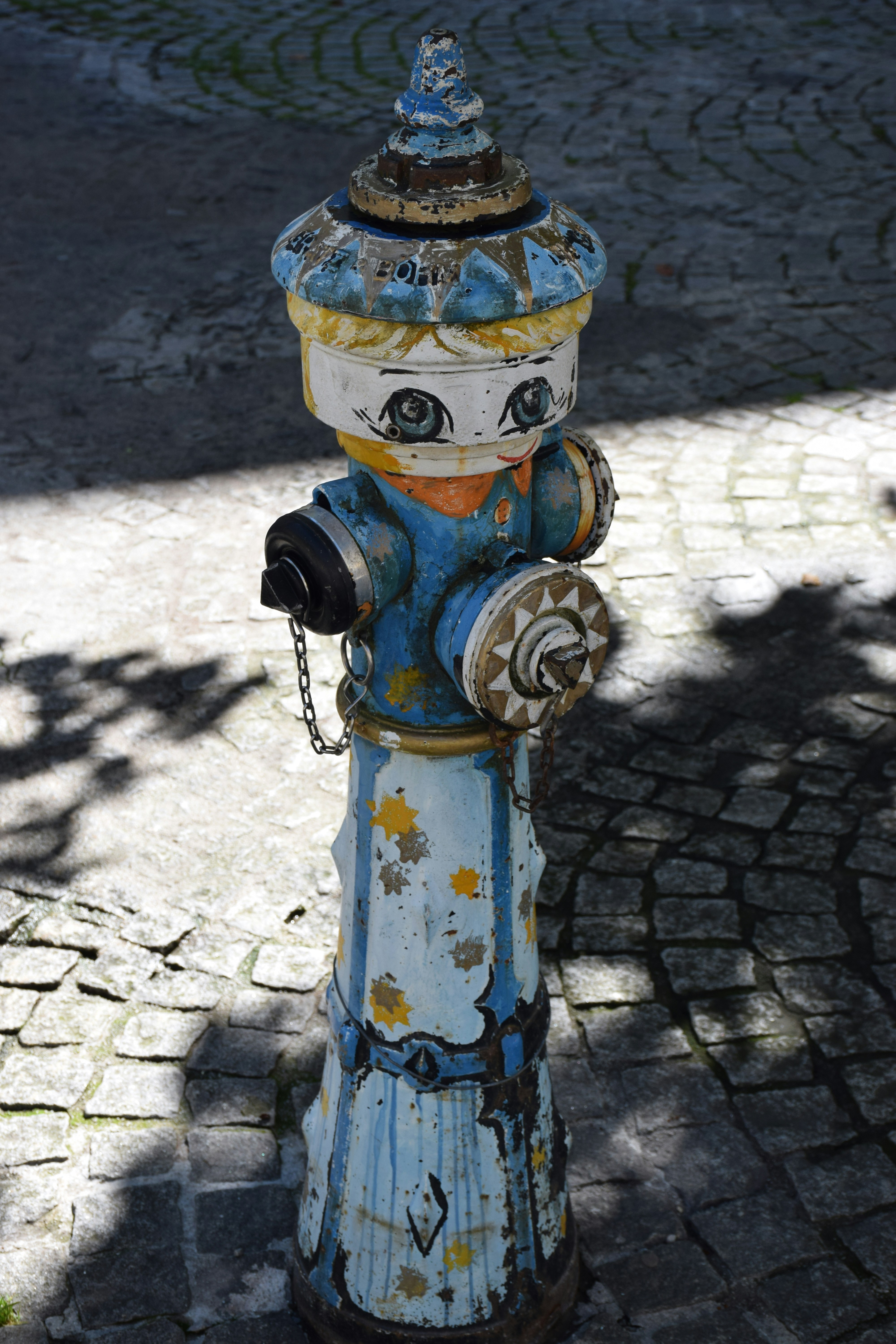Worn Fire Hydrant Marionette: A Sunlit Sentinel Amid Cobblestones