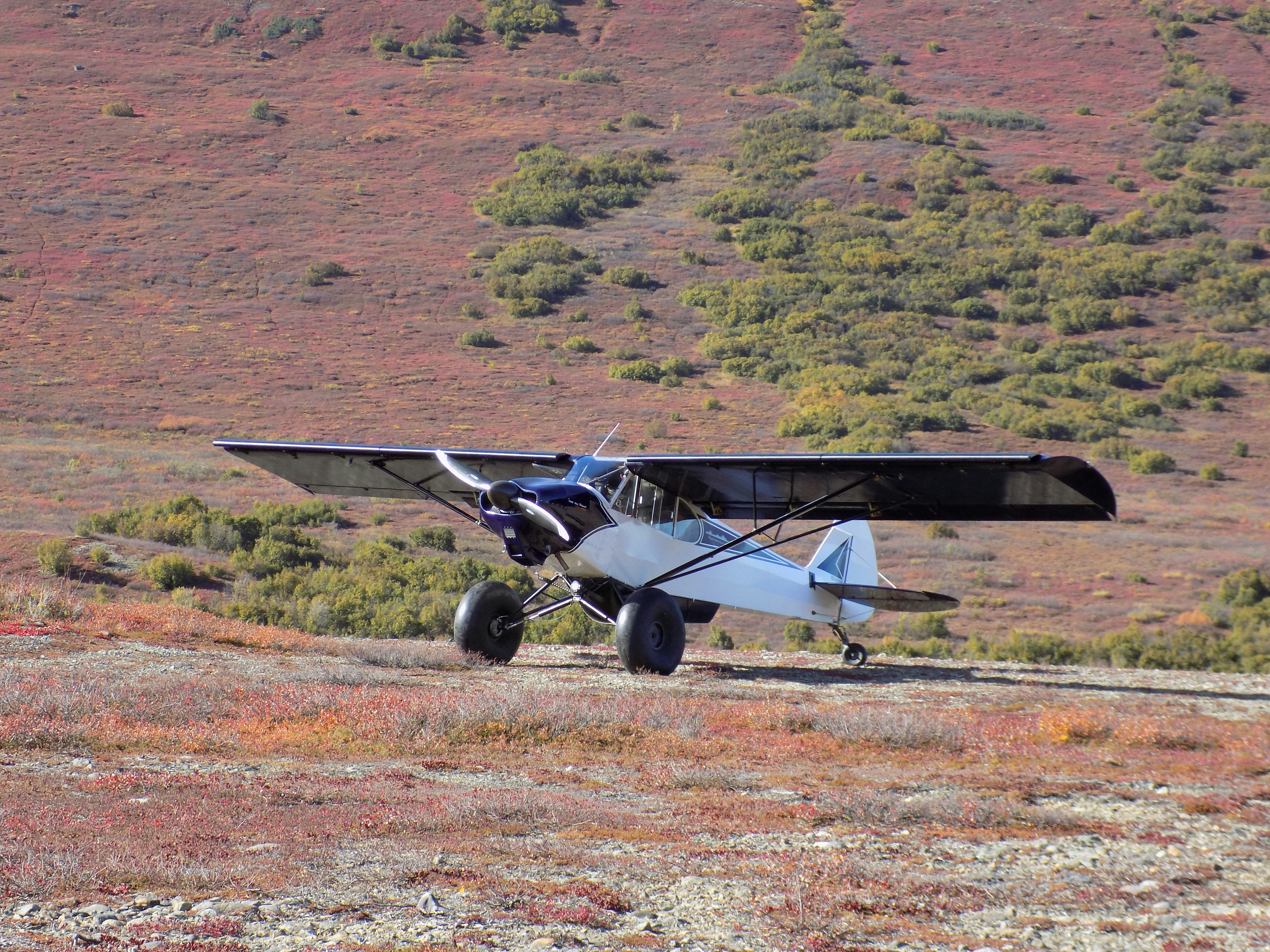 Light aircraft parked on vibrant autumn landscape, surrounded by rolling hills and colorful foliage.