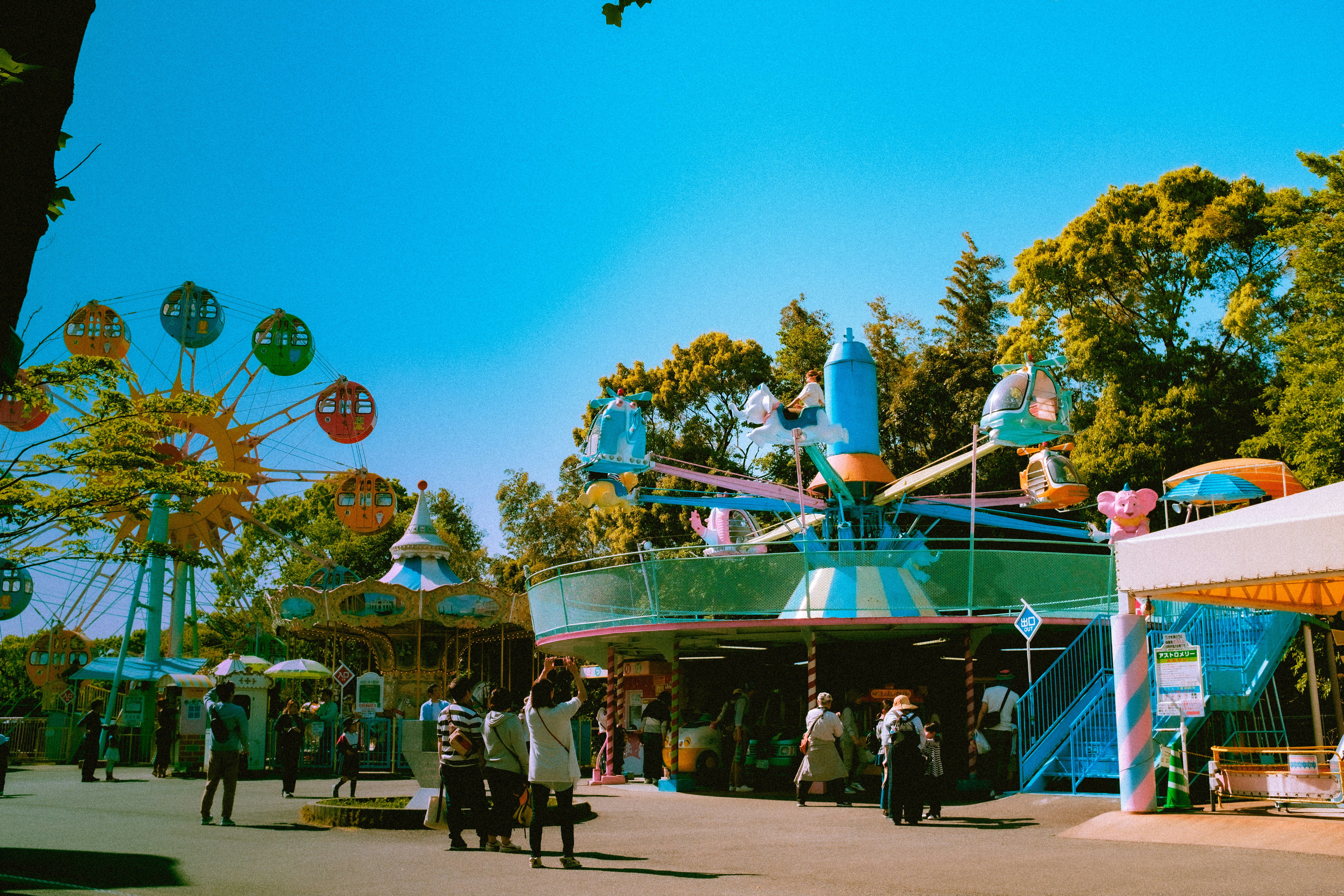 Colorful amusement park rides bustling with visitors under a clear blue sky. The vibrant scene showcases a lively atmosphere filled with joy and excitement.