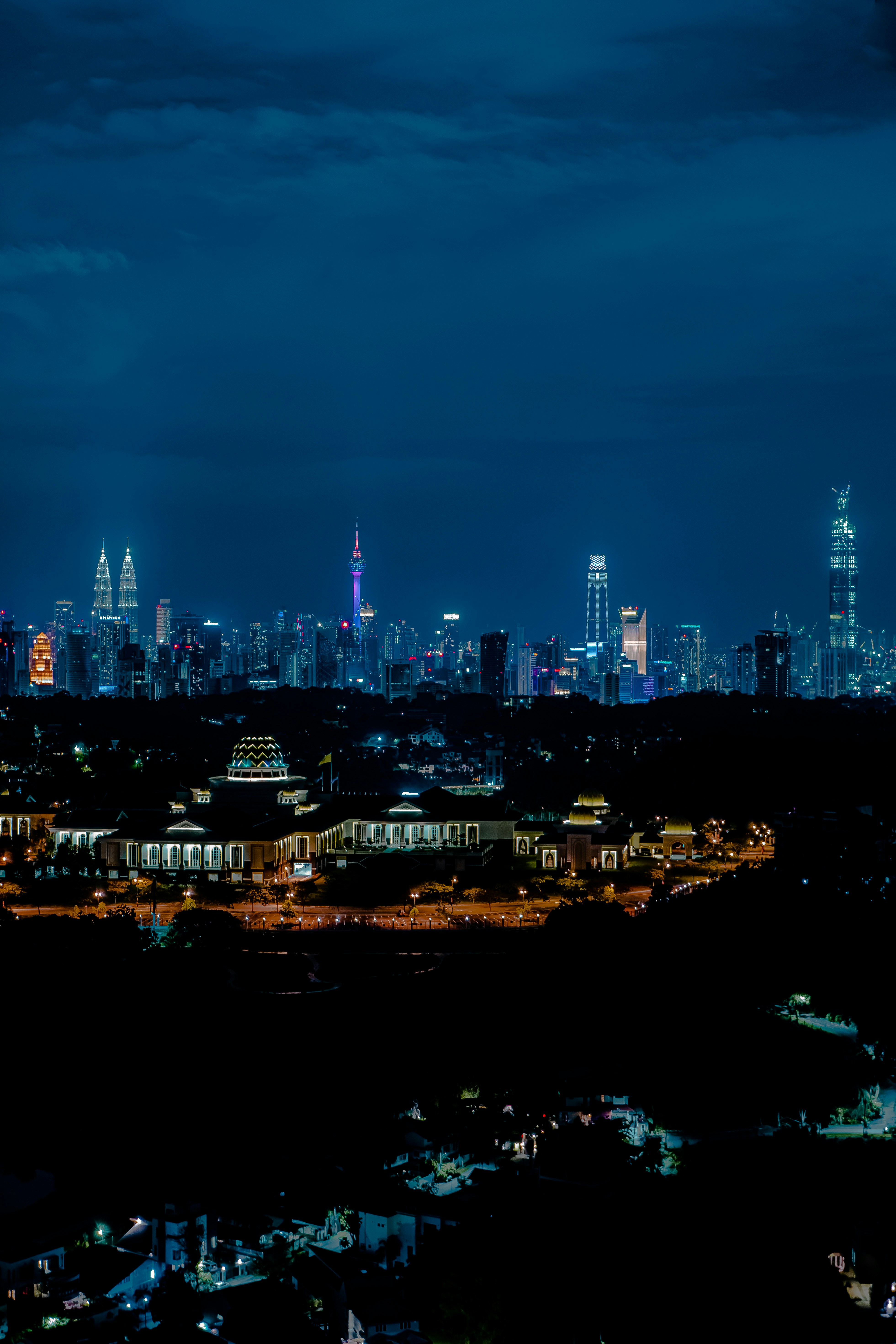 A panoramic view of a vibrant city skyline illuminated against a deep blue night sky, showcasing iconic skyscrapers and architectural landmarks.