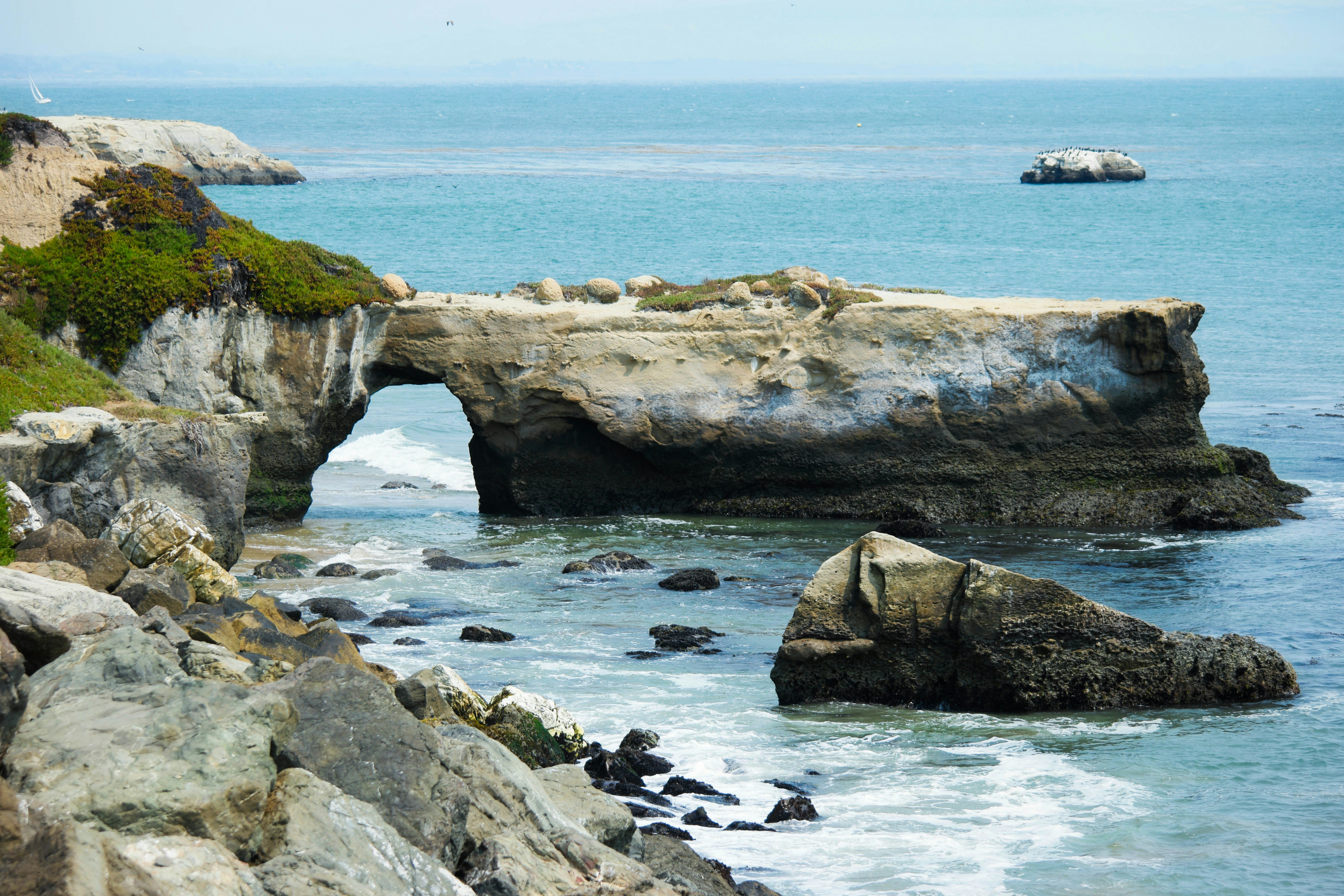 Natural rock arch over ocean waves with rugged cliffs and distant rocks.