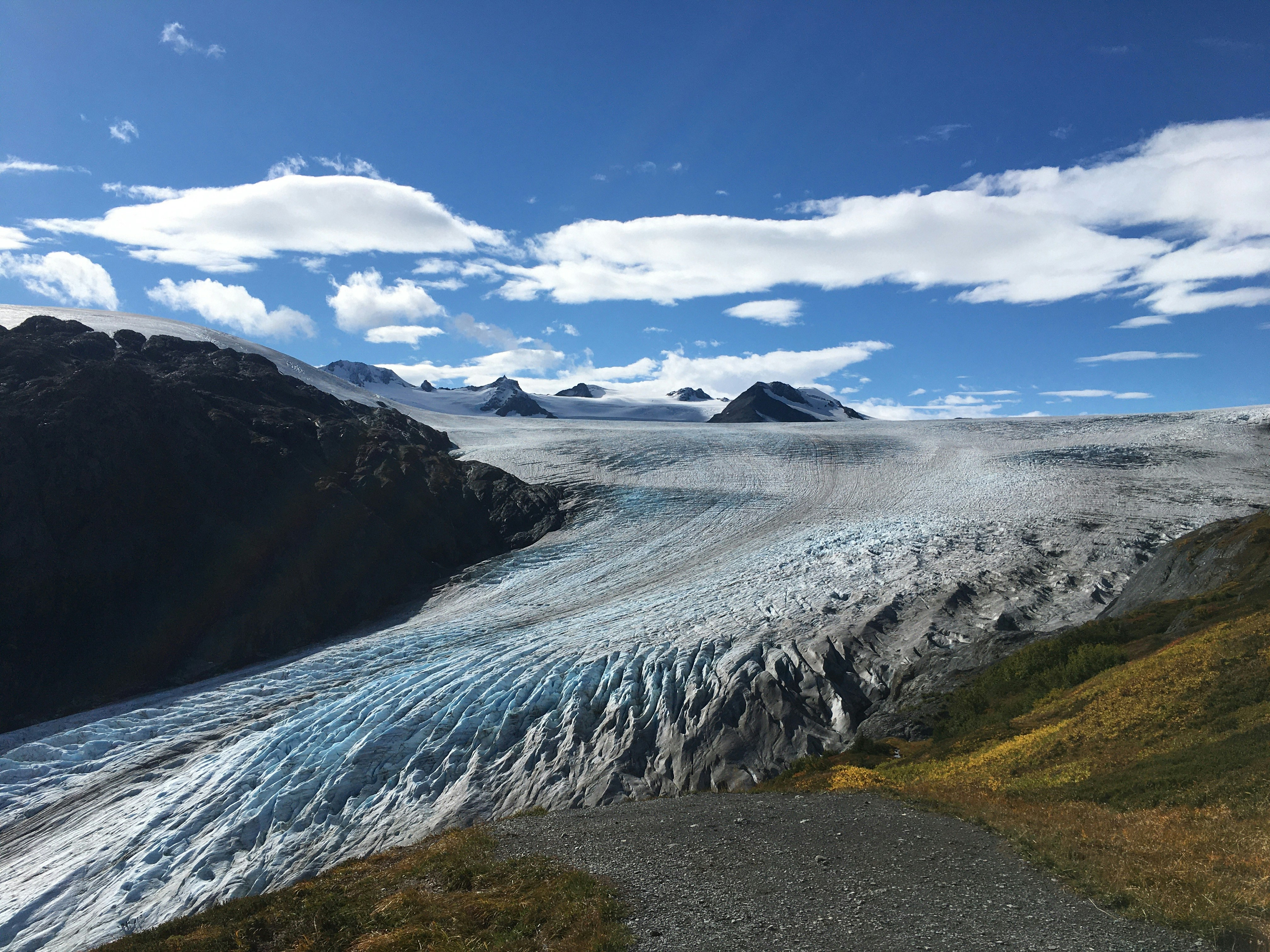 Expansive glacier flowing down from rugged mountains under a bright blue sky, showcasing intricate ice patterns and textures.