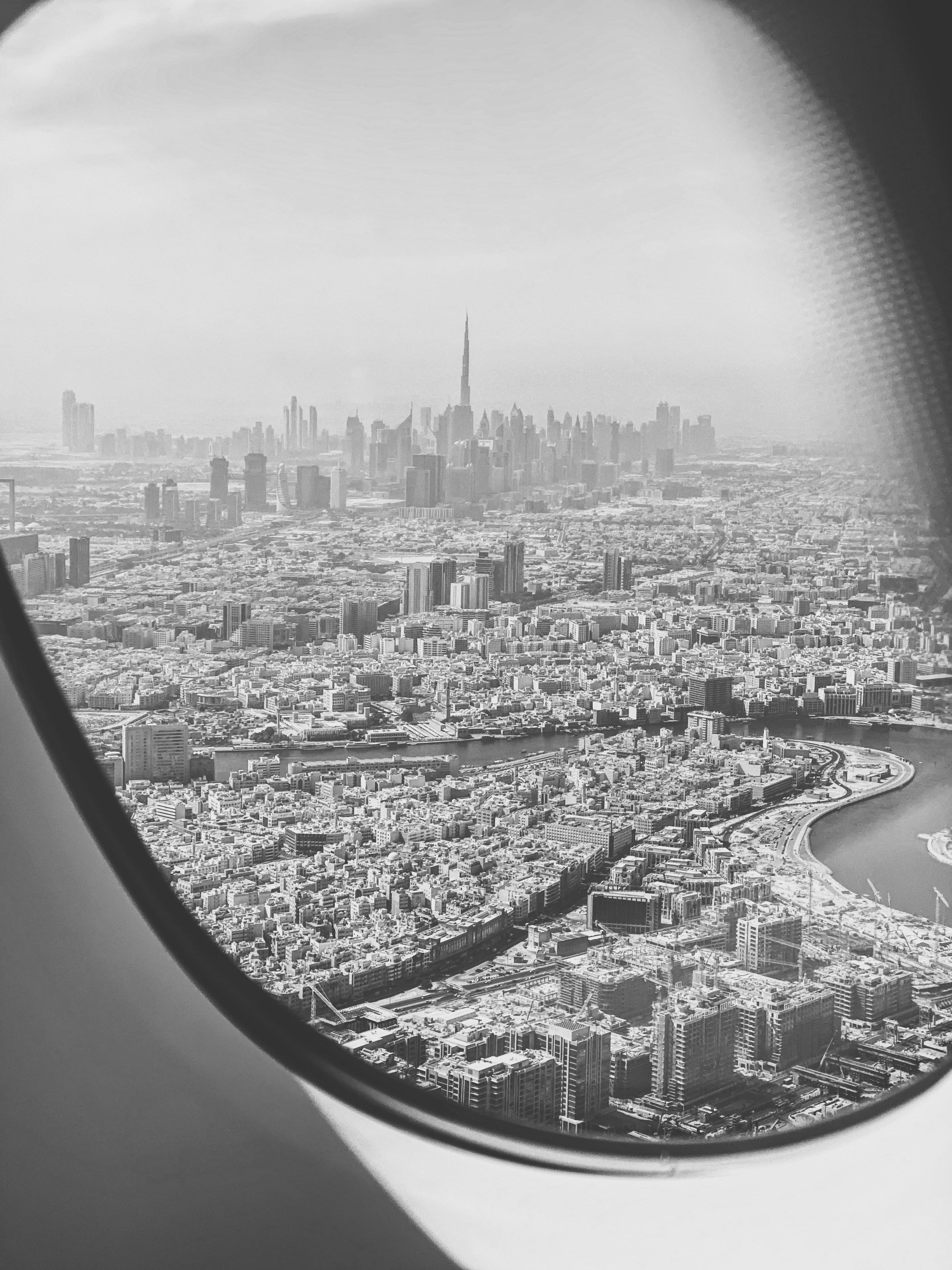 Aerial view of a sprawling cityscape framed by an airplane window, showcasing intricate urban patterns and the iconic skyline in the distance.