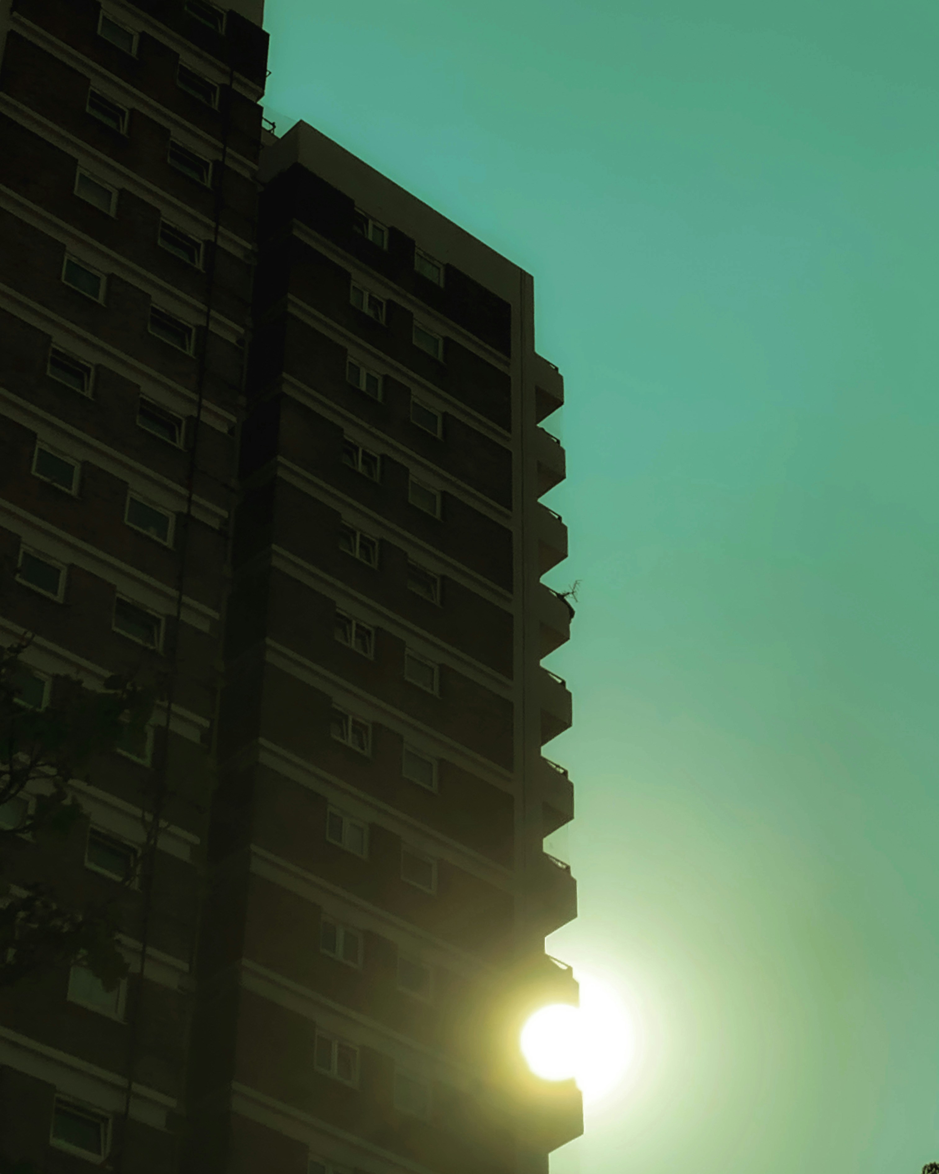 Mint Dusk Over a High-Rise Silhouette with a Peeking Sun