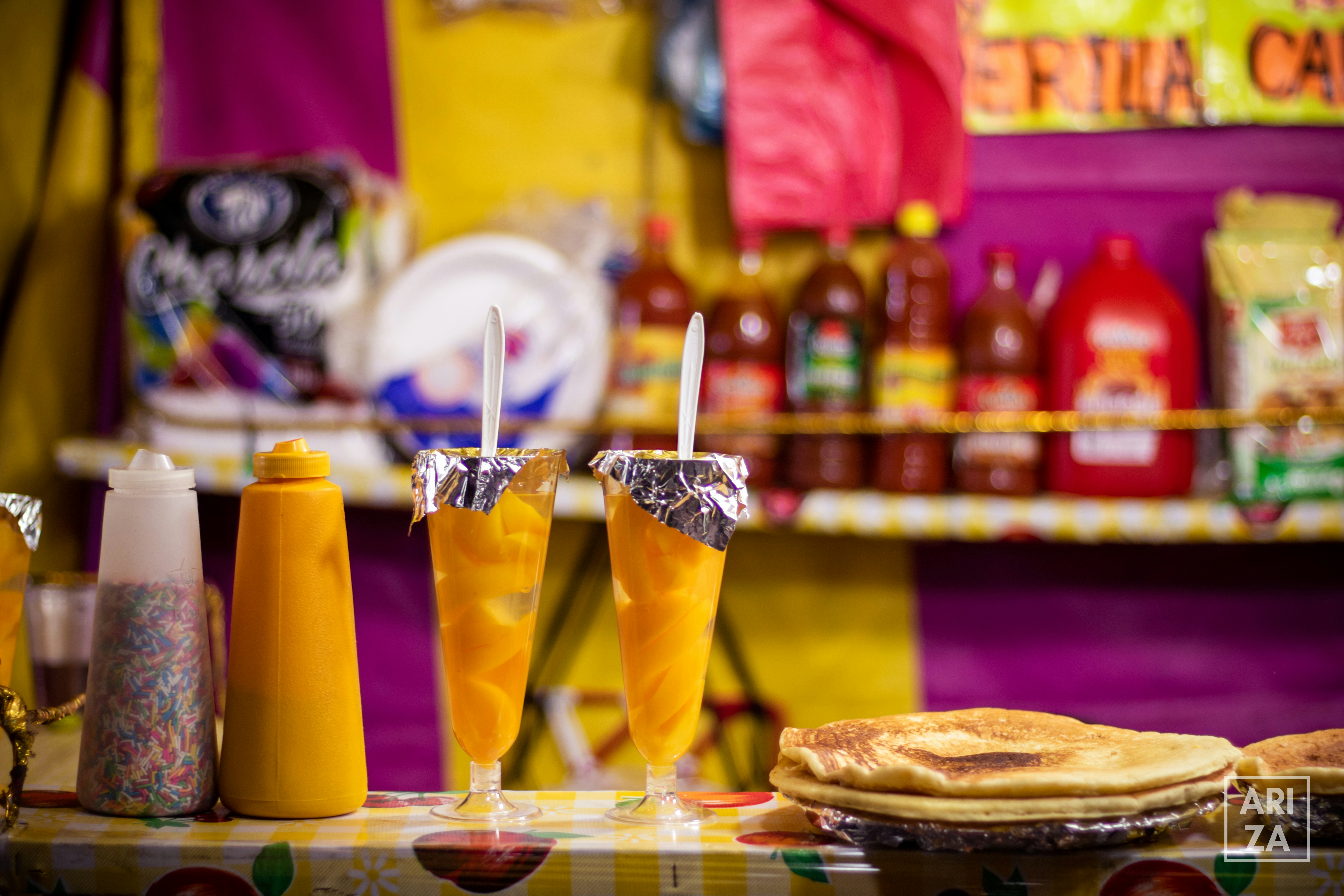 Brightly colored snack stand with yellow drinks and condiments under festive lighting.