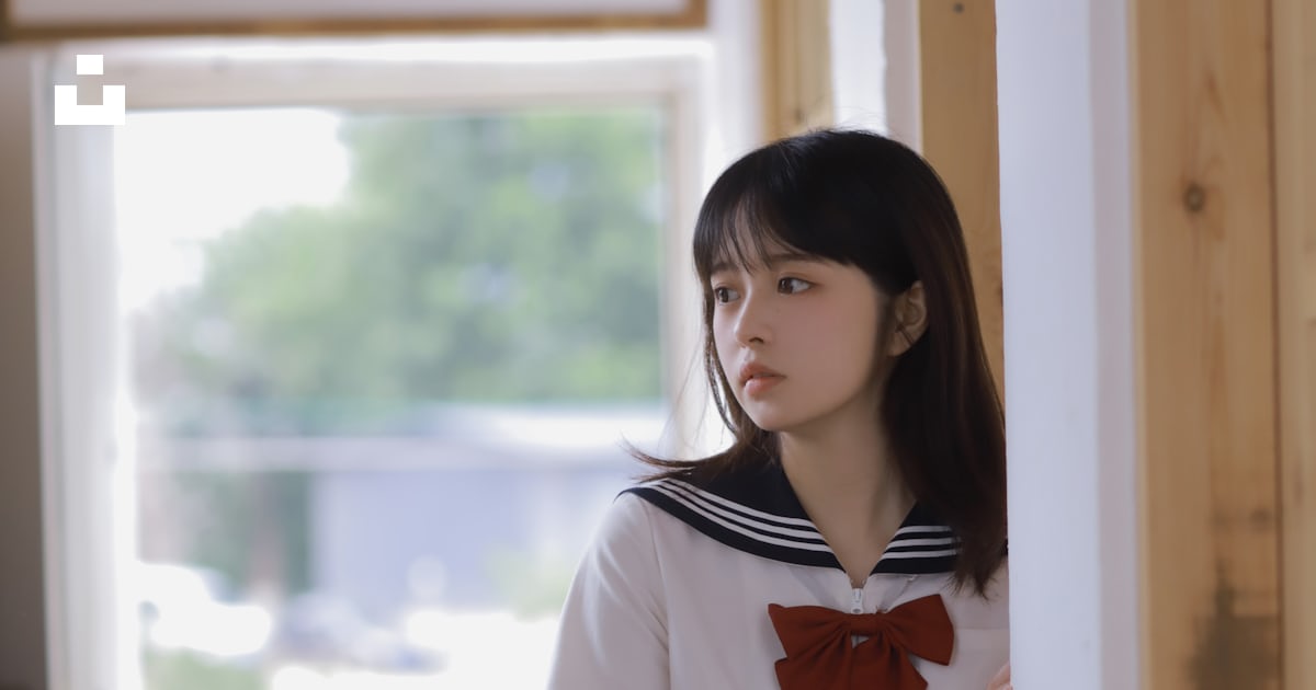 낮 동안 창문 옆에 서 있는 흰색과 검은색 교복을 입은 여자 사진 Unsplash의 무료 의복 이미지