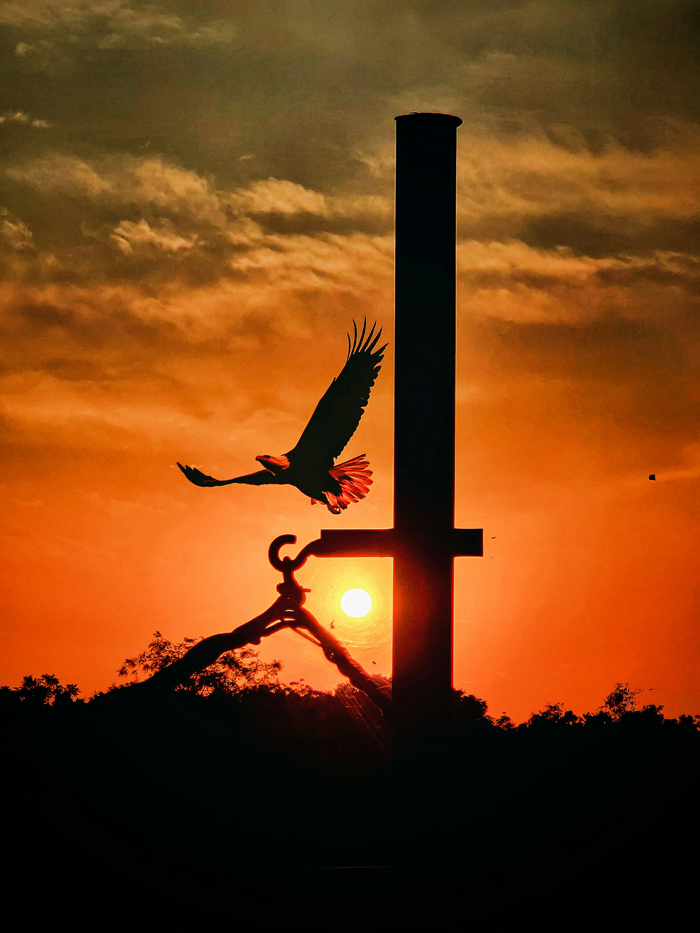 Silhouette of an eagle soaring near a cross as the sun sets, casting a warm glow across the sky.