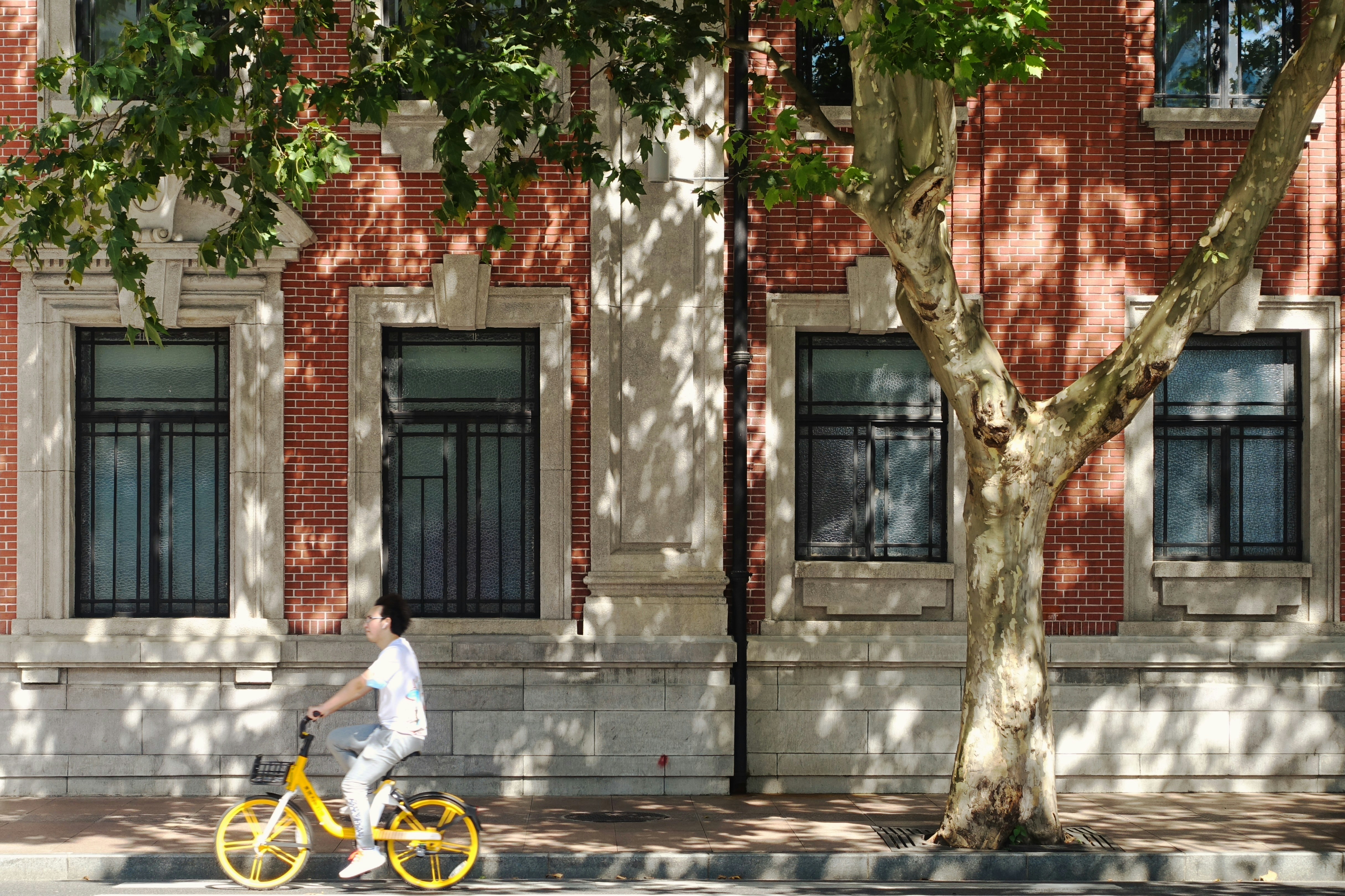 Yellow Bicycle on a Sun-Drenched City Street Before a Shadow-Dappled Brick Facade