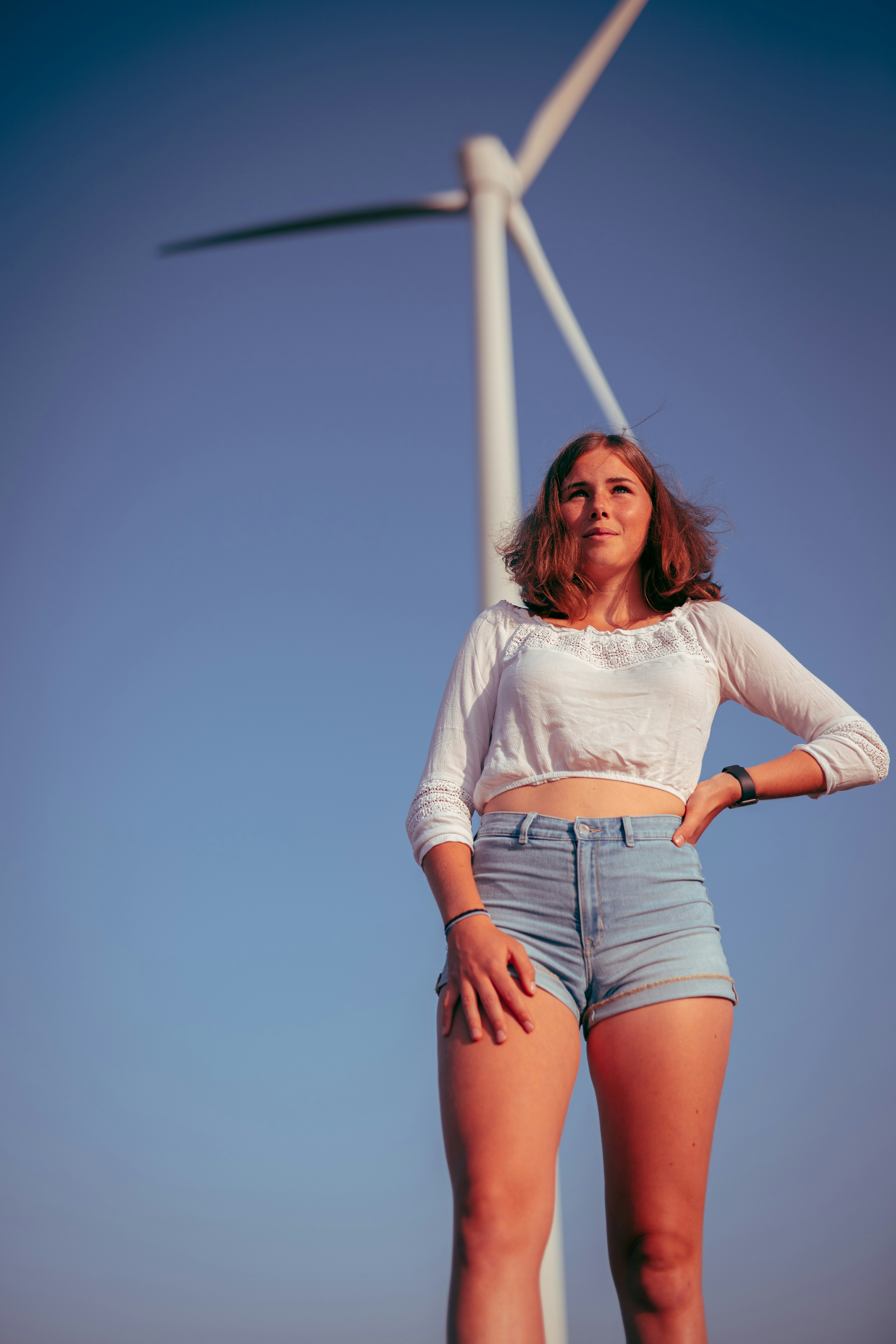 woman in white long sleeve shirt and blue denim daisy dukes standing beside white metal pole